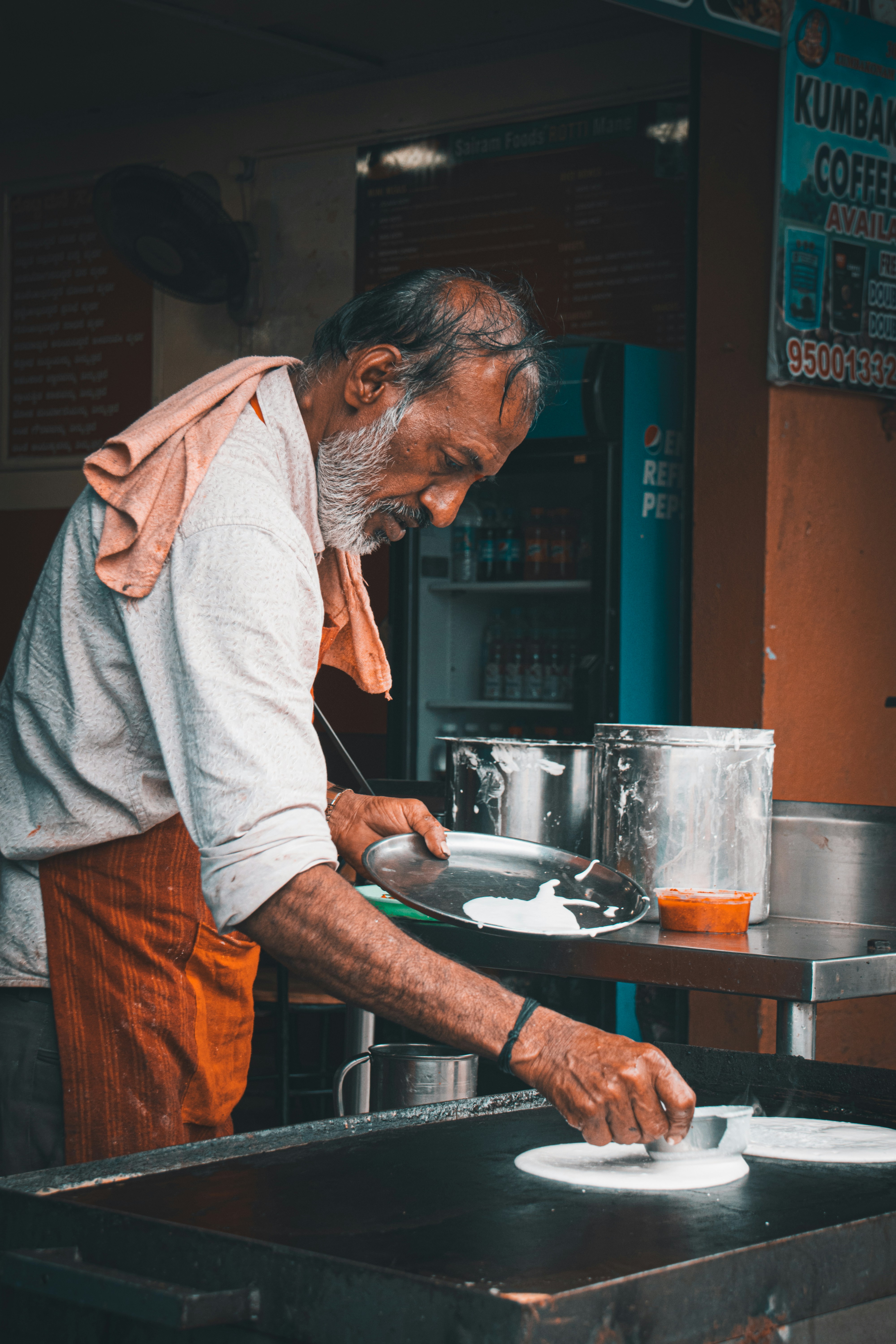 Elderly man cooking dosas at a street food stall.