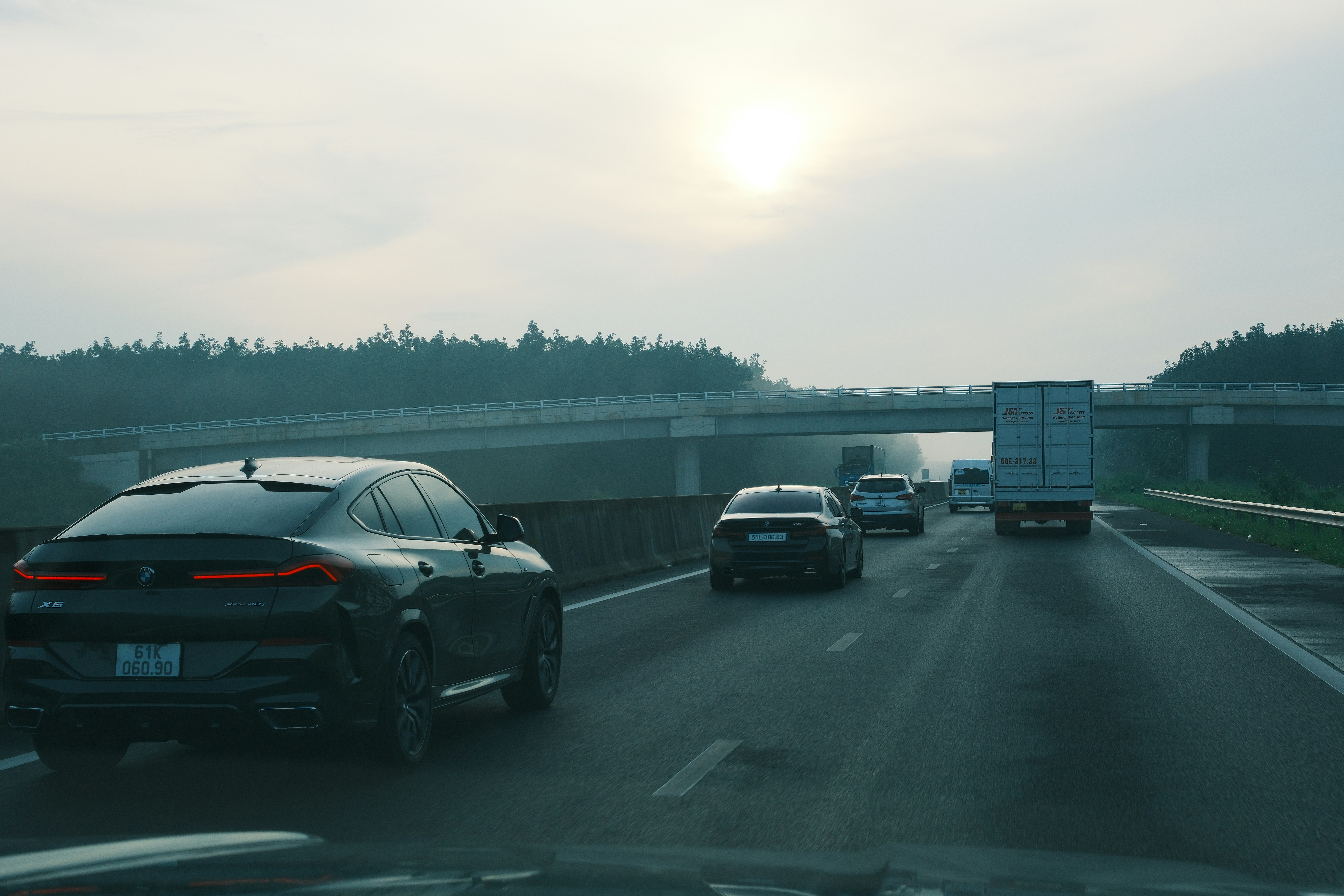 Cars driving on a highway under a hazy sun.