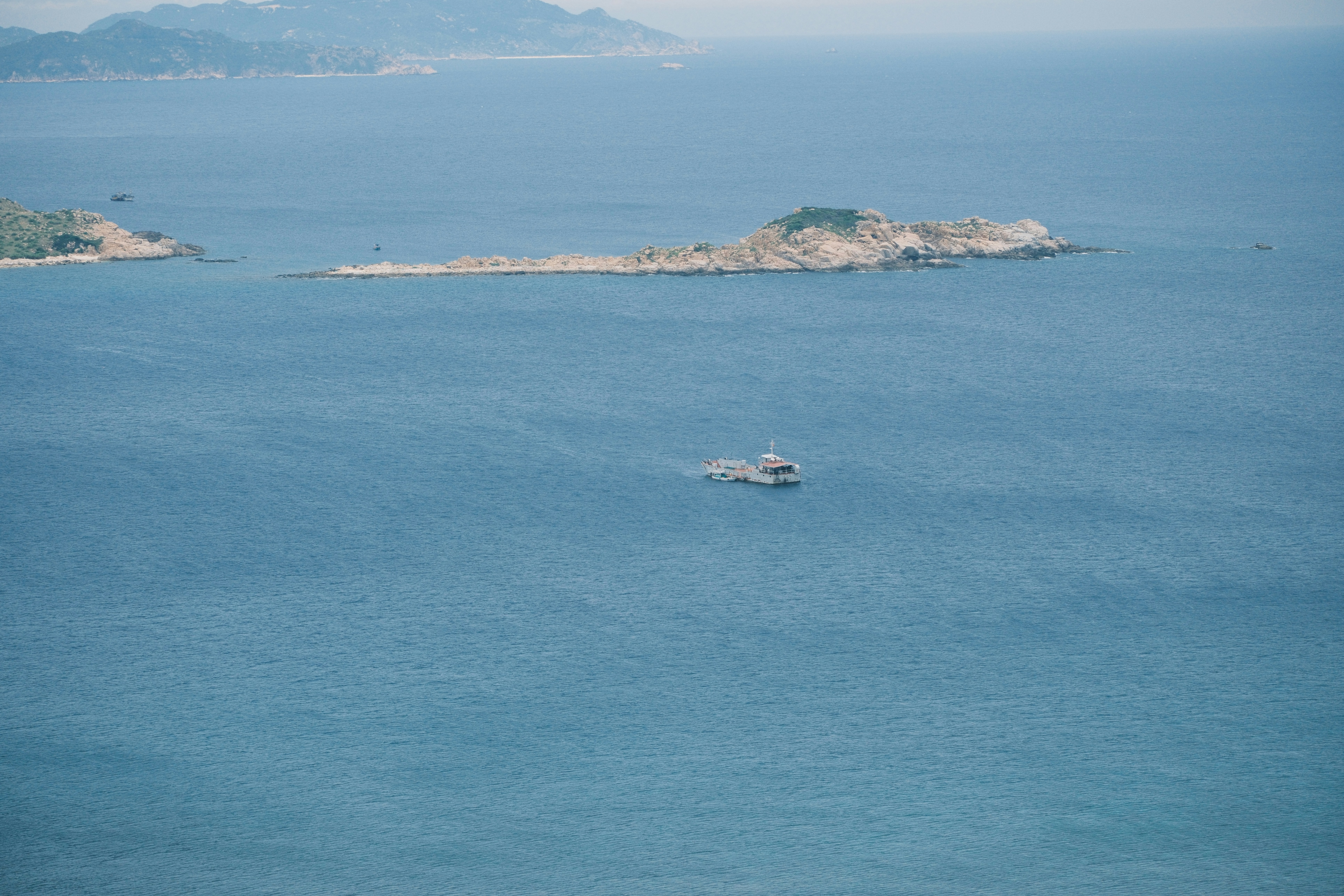 A solitary fishing boat navigates the calm blue waters, surrounded by distant islands under a clear sky.