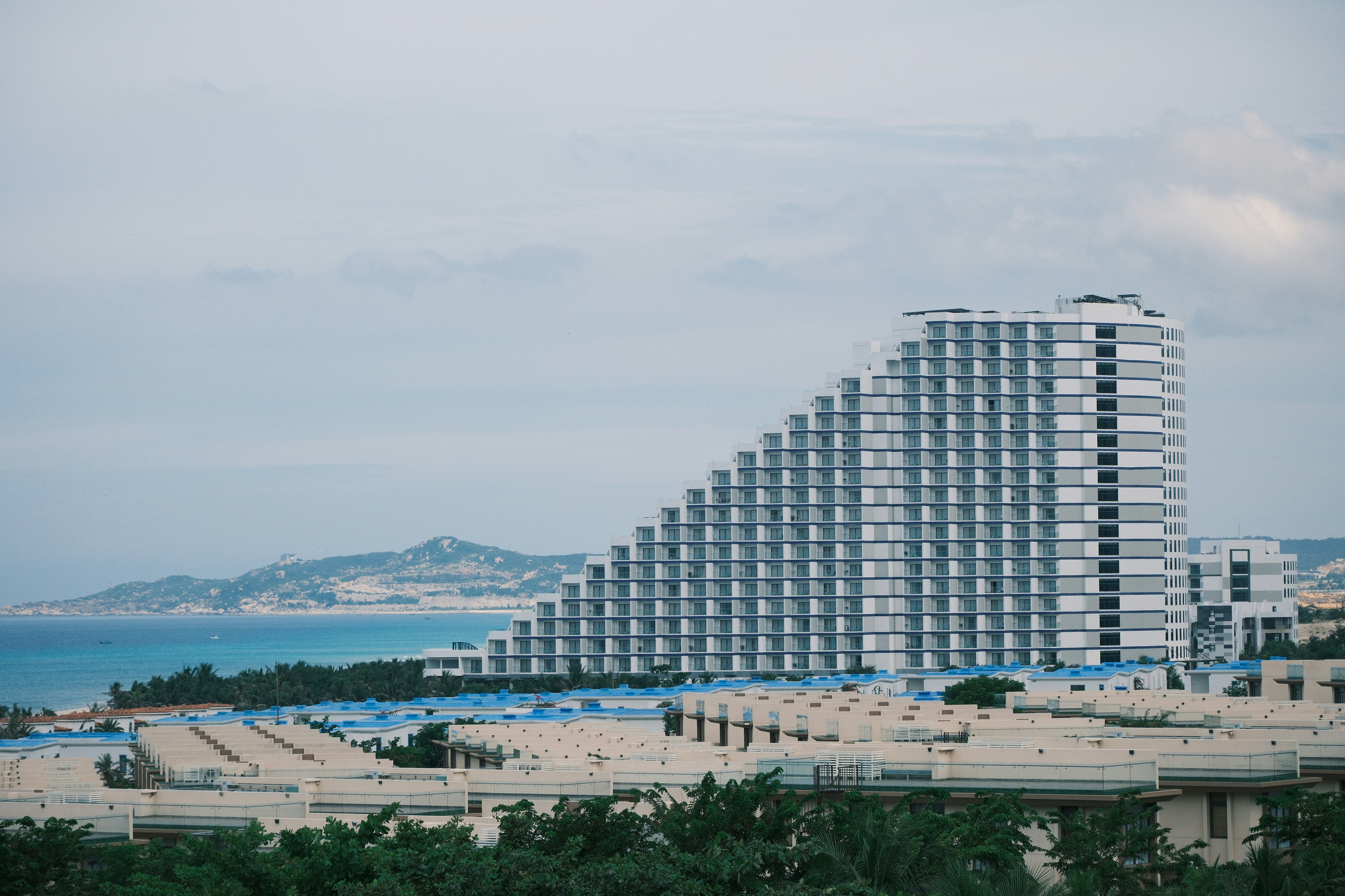 Modern high-rise building set against a coastal backdrop, showcasing a unique geometric design. The scene captures the blend of urban architecture and natural beauty.