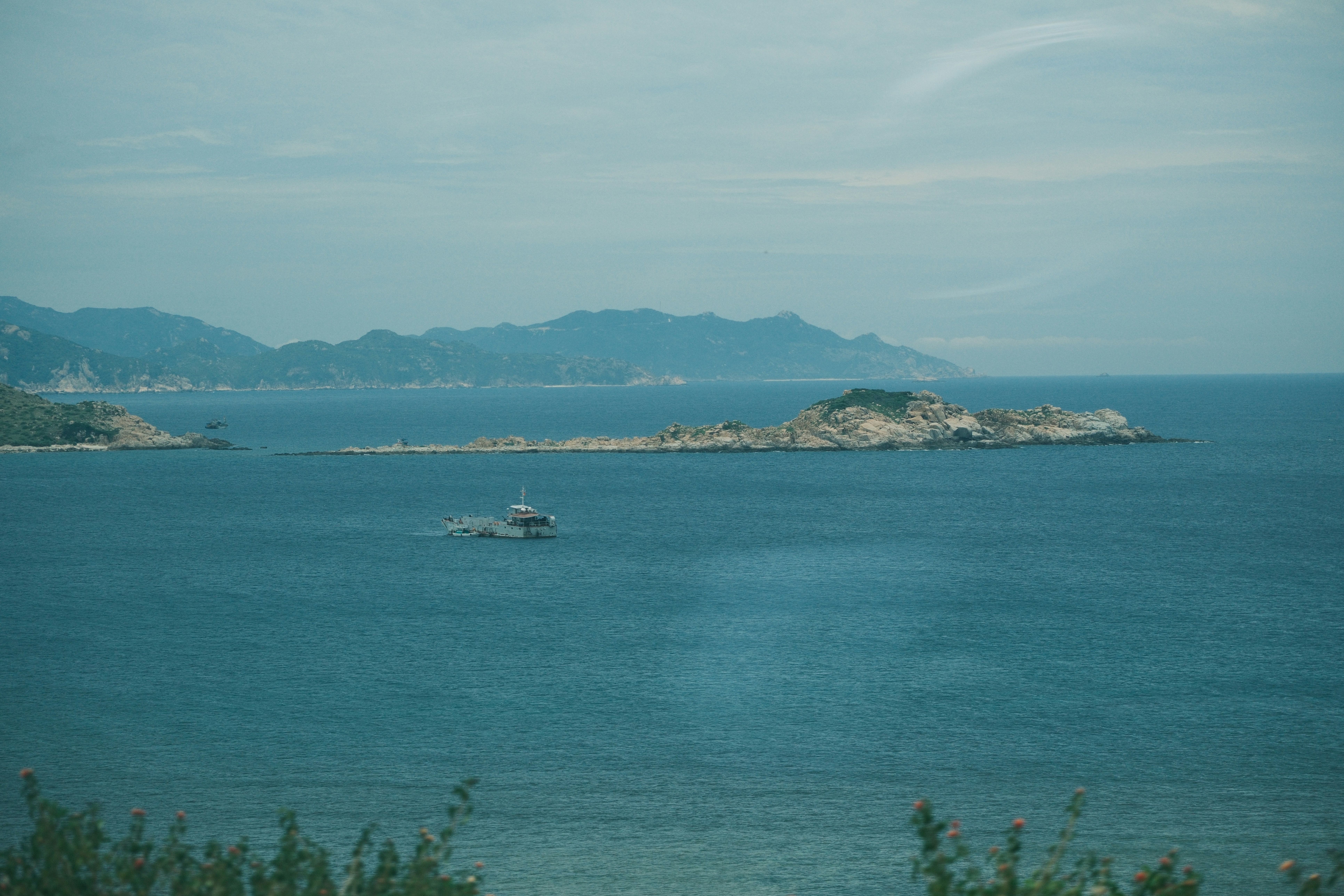 A boat sails on the blue sea near islands.
