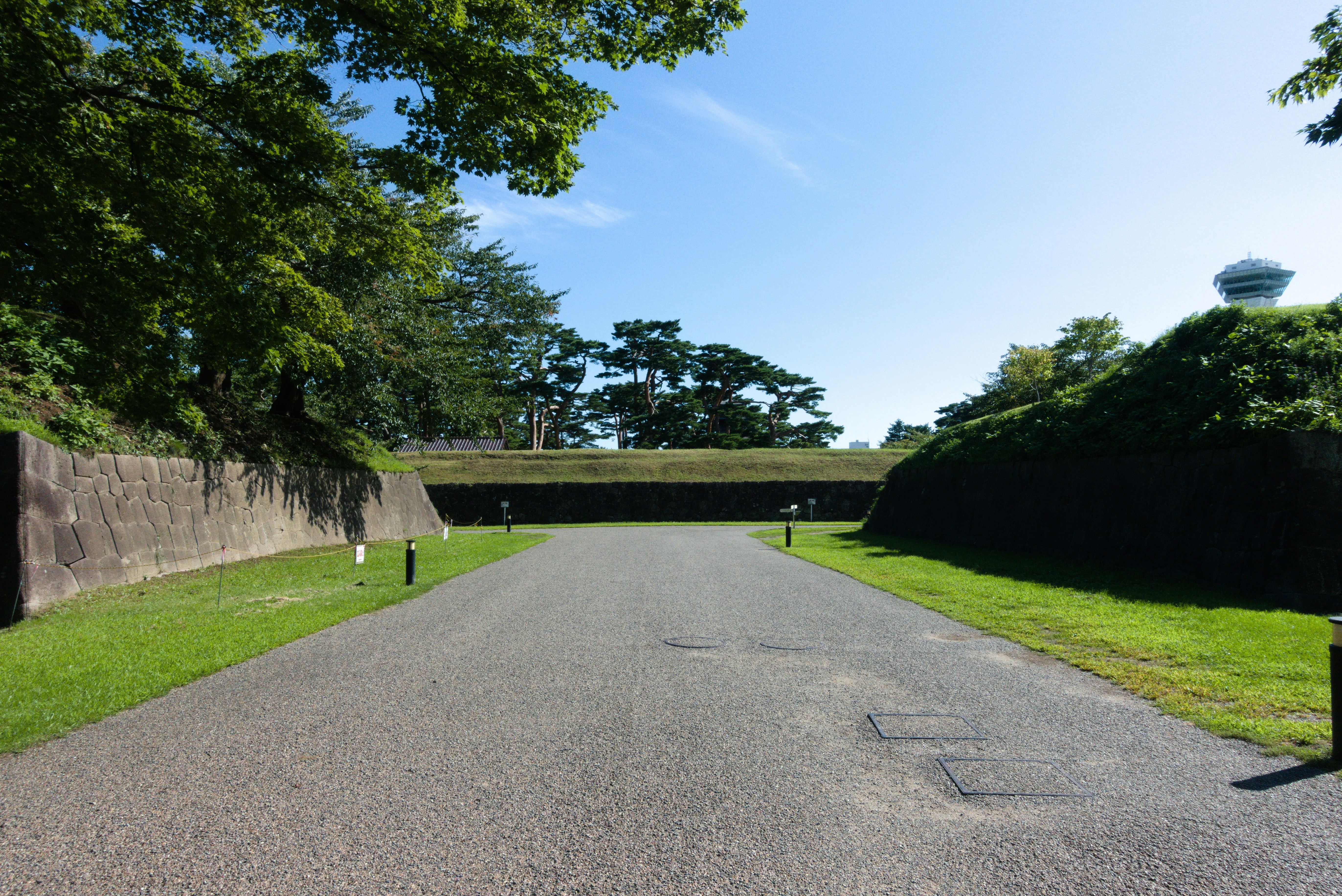 A paved road leads through grassy embankments under blue sky.