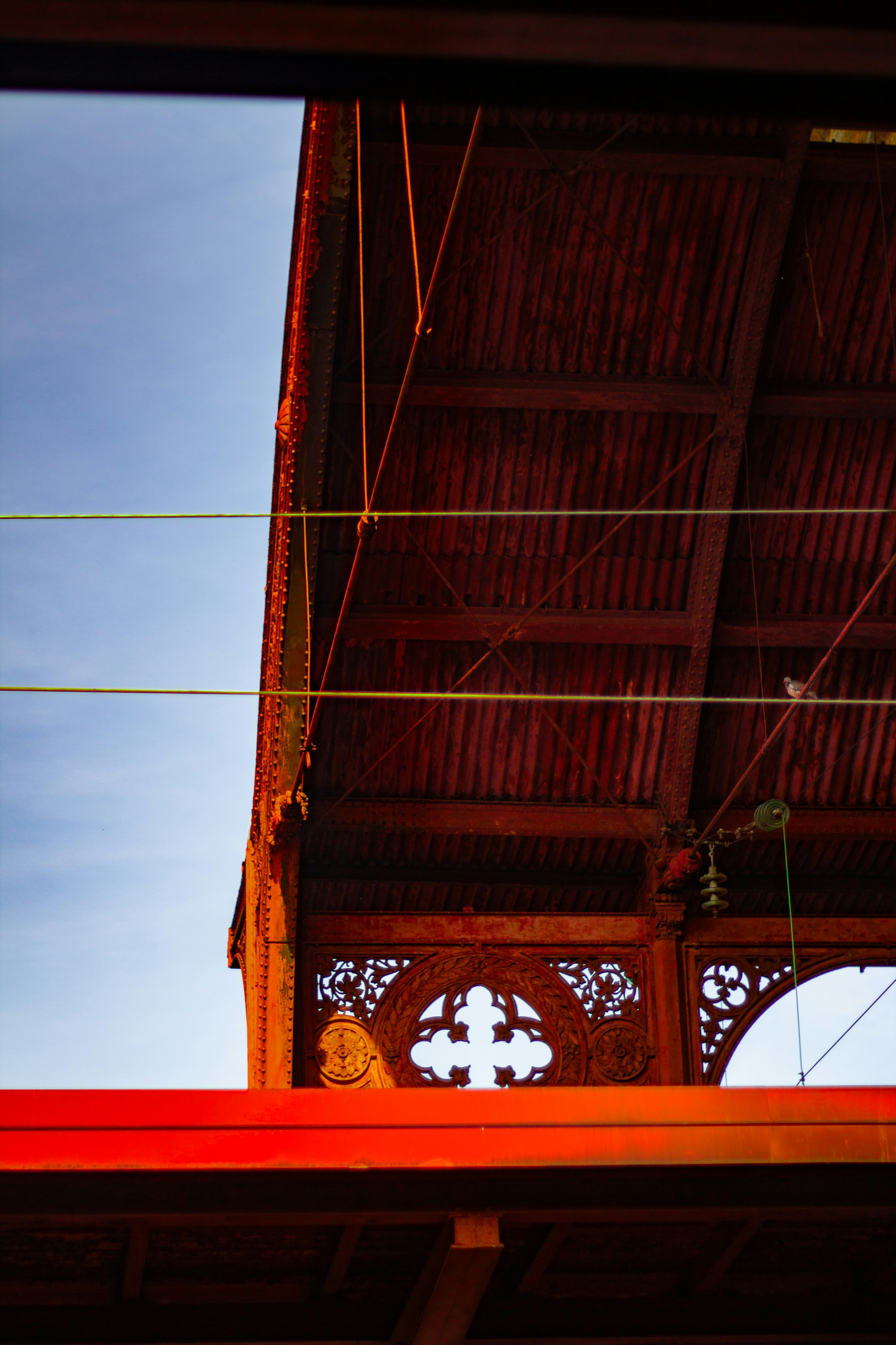 Lacework Under a Crimson Rail: Timber Roof Framing Against the Sky