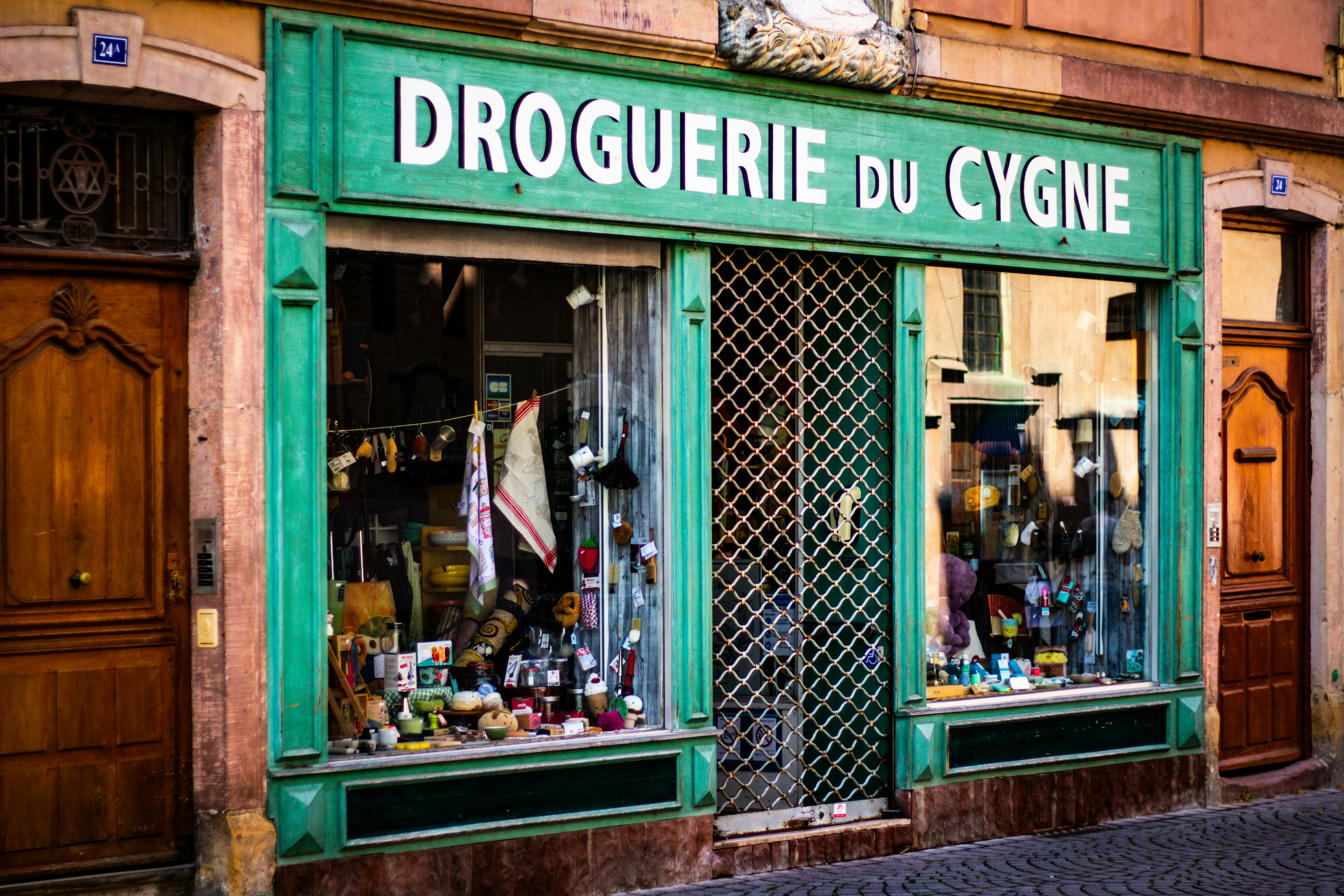 Quaint storefront of 'Droguerie du Cygne' showcasing an array of colorful goods behind a decorative metal grate.