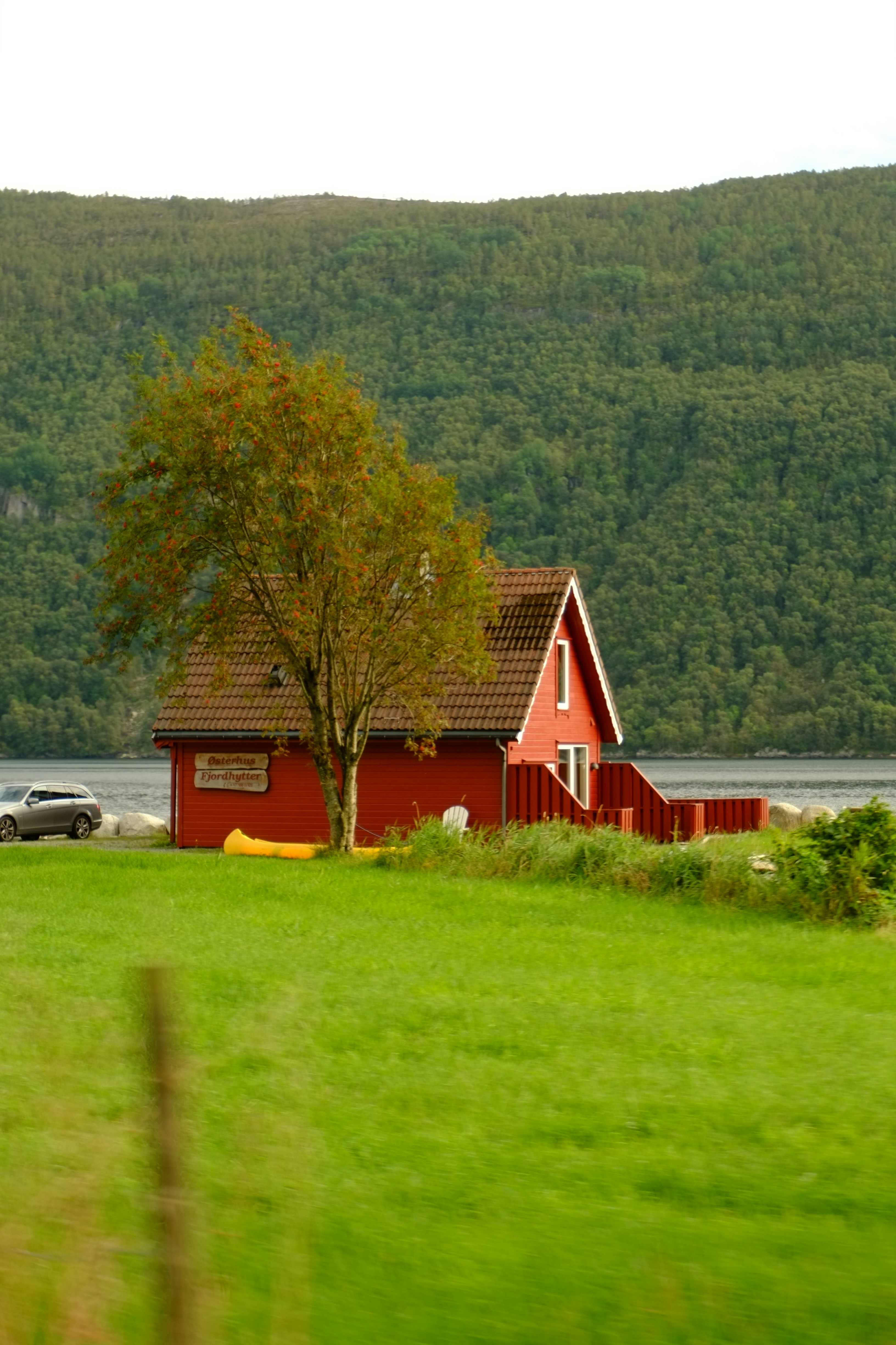 Red house by a lake with green hills.