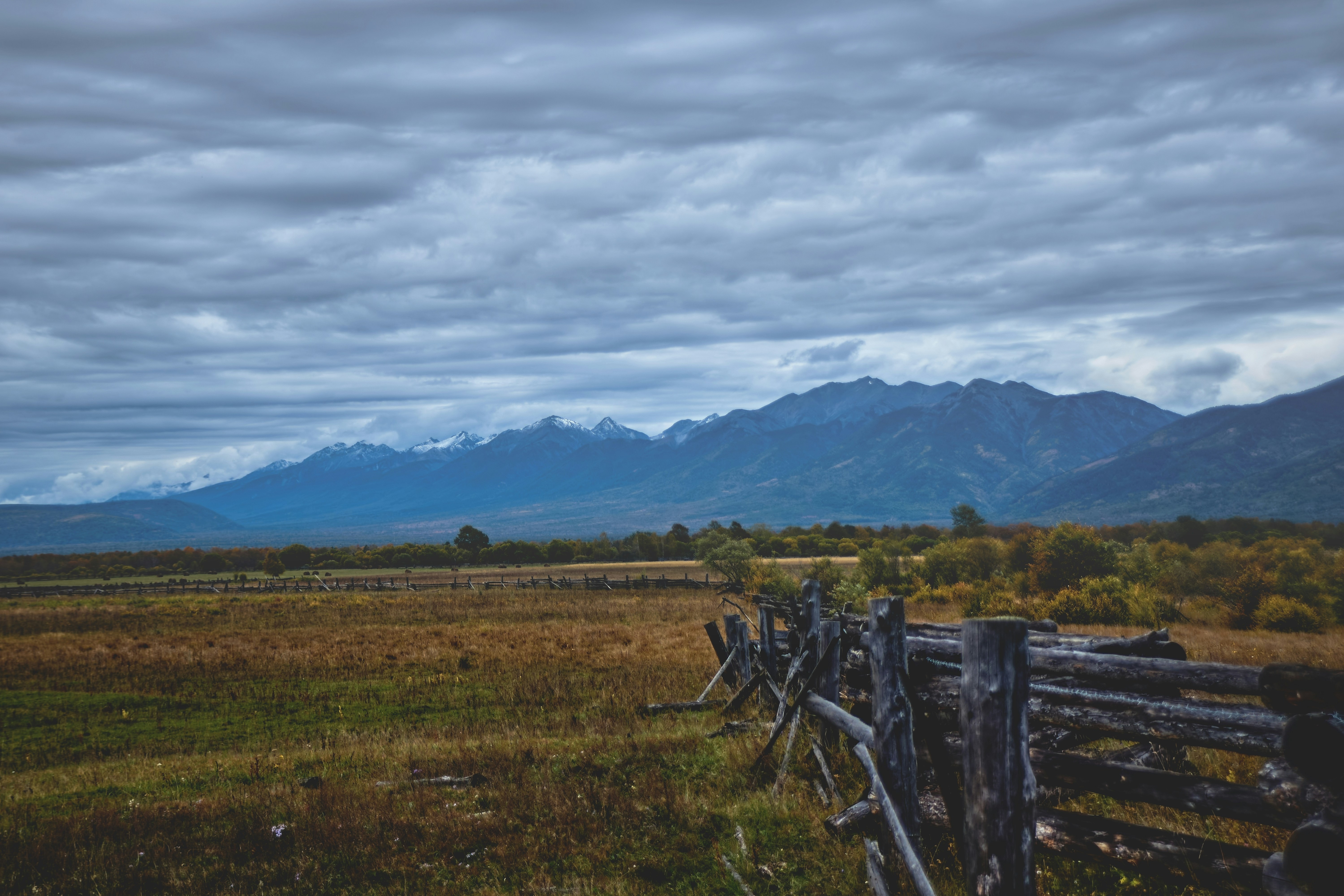 Wooden fence in field with mountains under cloudy sky