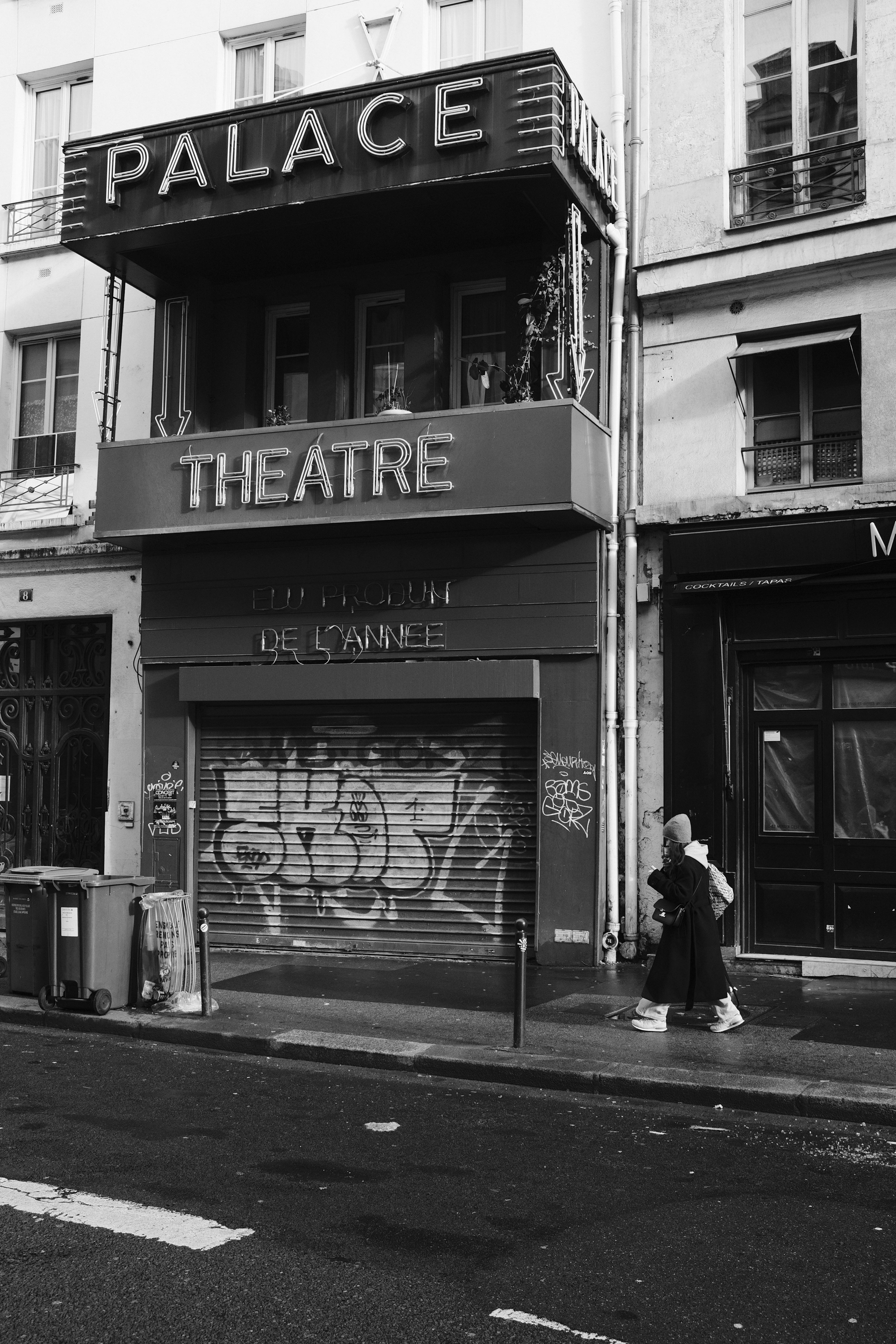 A person walks past a closed theatre with graffiti.