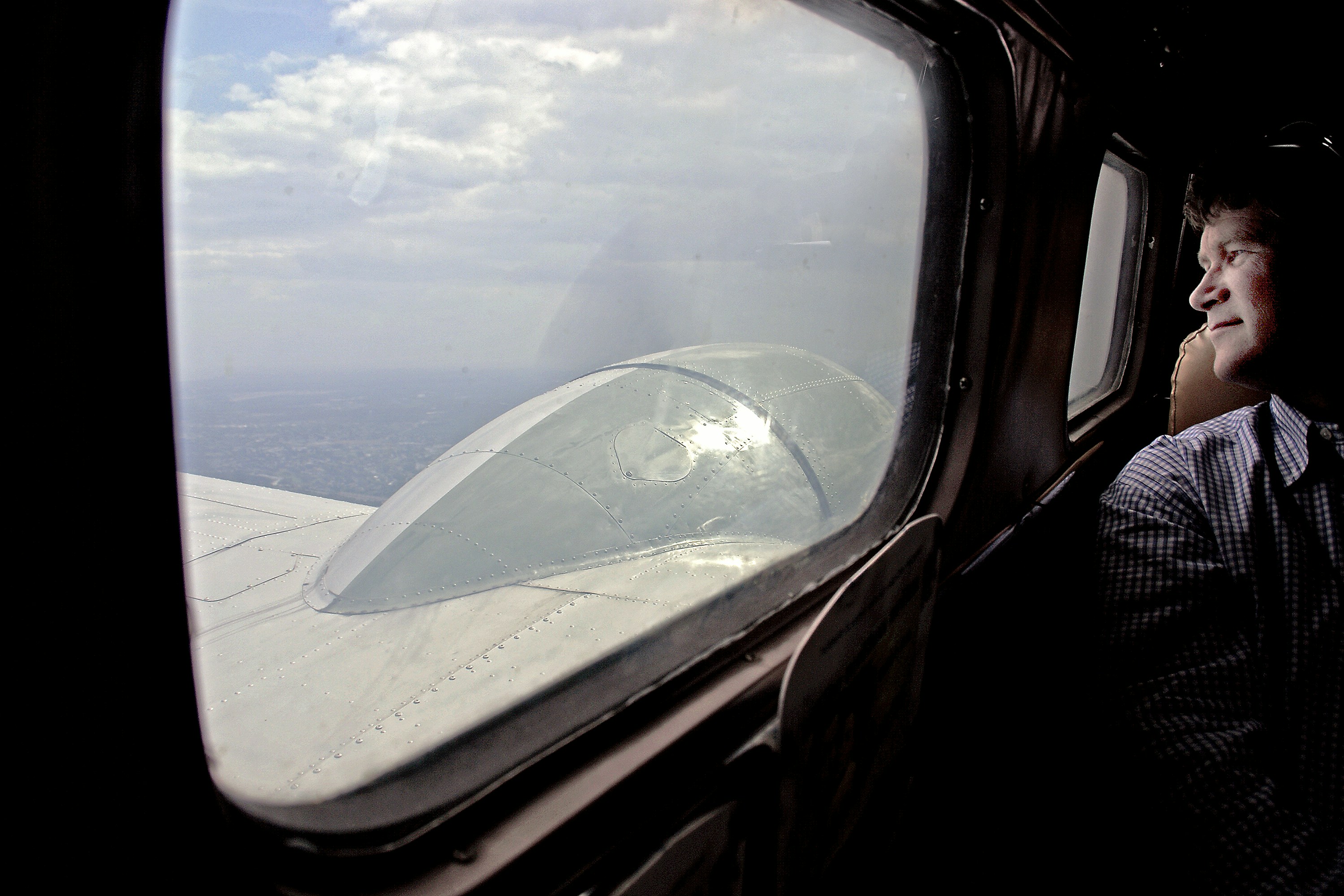 It seems like the passenger in the window seat is deep in thought. | Man looking out airplane window at clouds