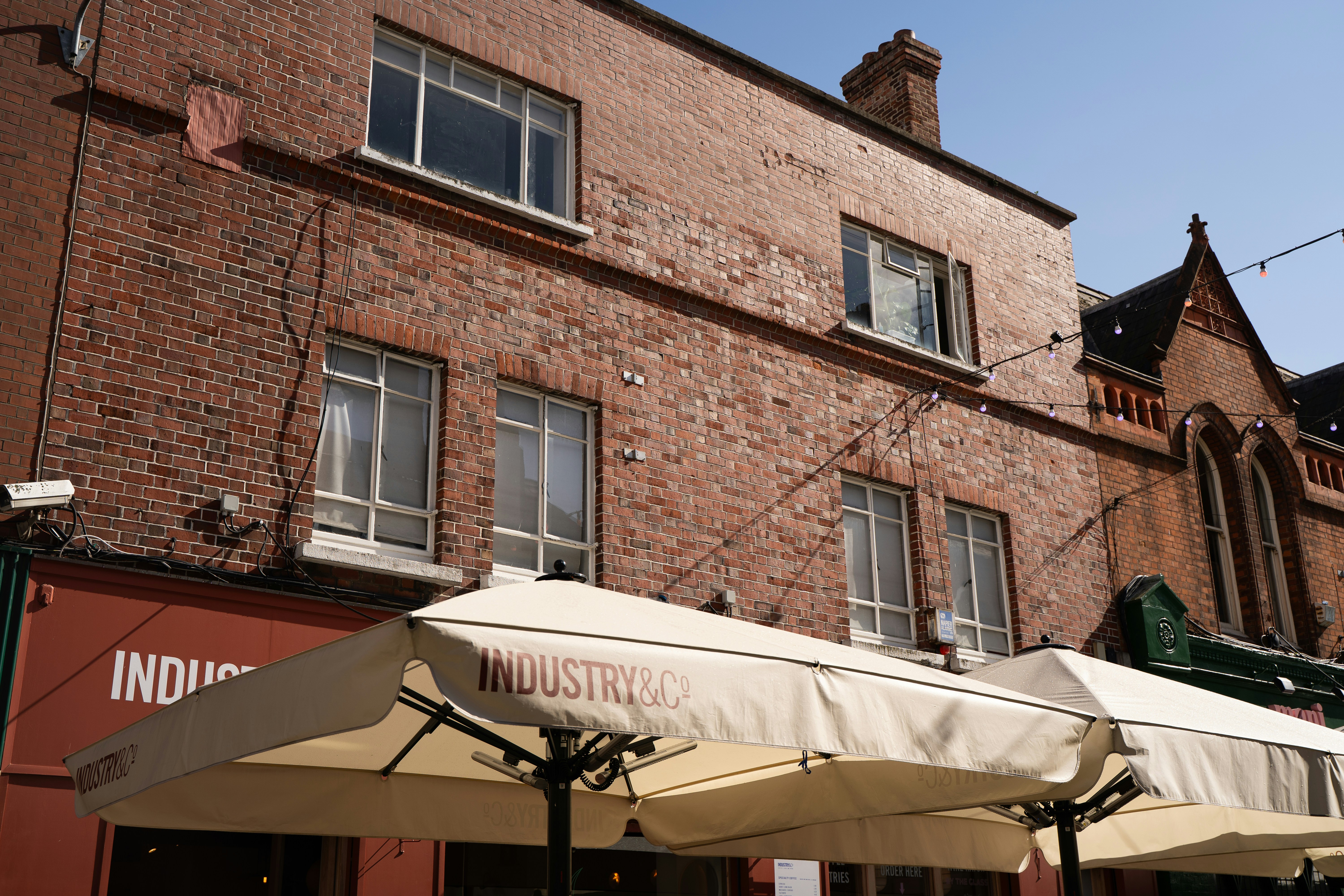 Sunlit Café Terrace Under a Brick-Fronted Street Canopy