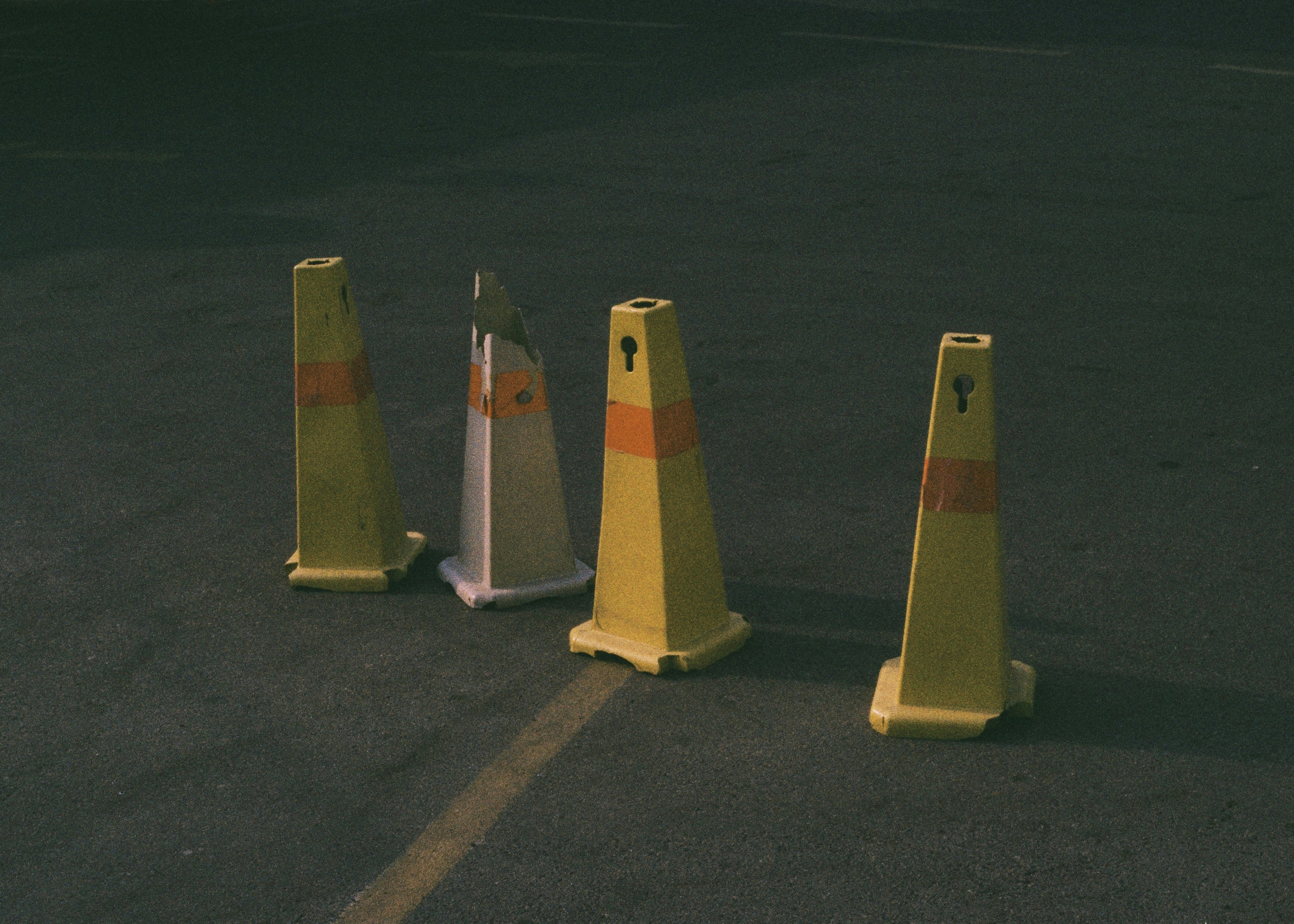 Four traffic cones arranged in a semi-circle on asphalt, with one cone showing signs of wear. The scene captures a moment of urban stillness.