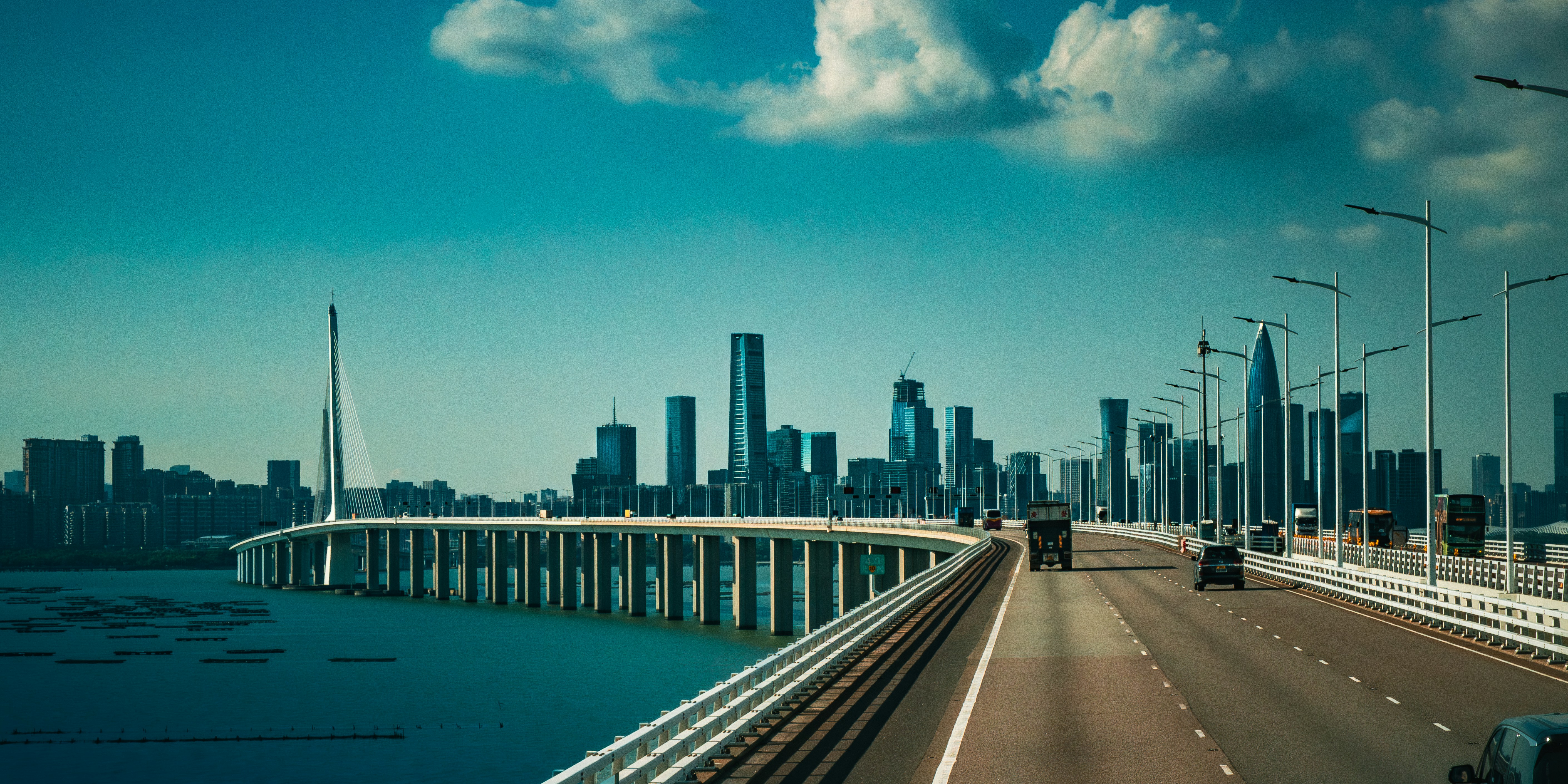 A modern bridge curves gracefully over a serene body of water, framed by a skyline of towering skyscrapers under a vibrant sky.