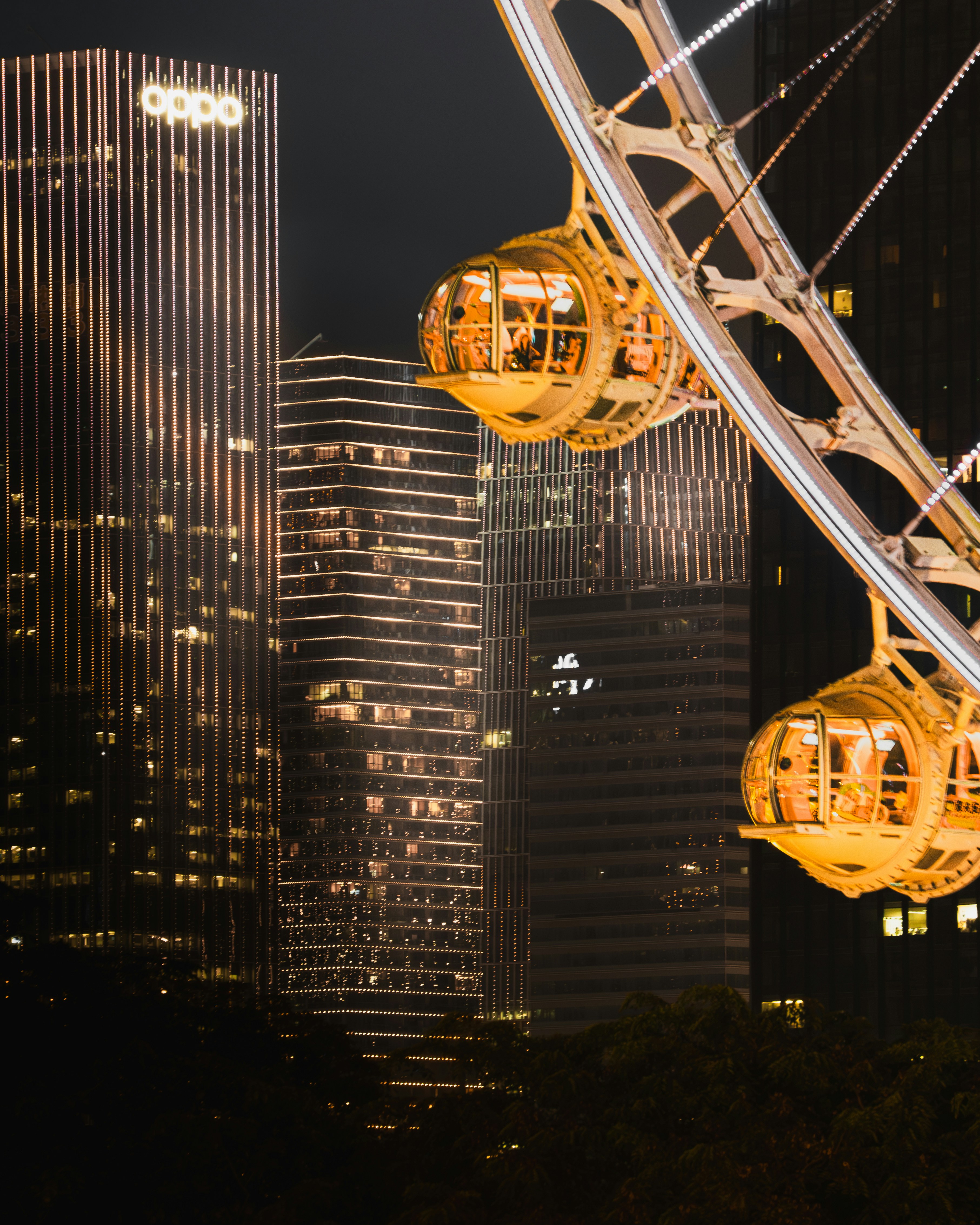 Ferris wheel cabins illuminated against a backdrop of skyscrapers adorned with lights. The scene captures the vibrant energy of urban nightlife.