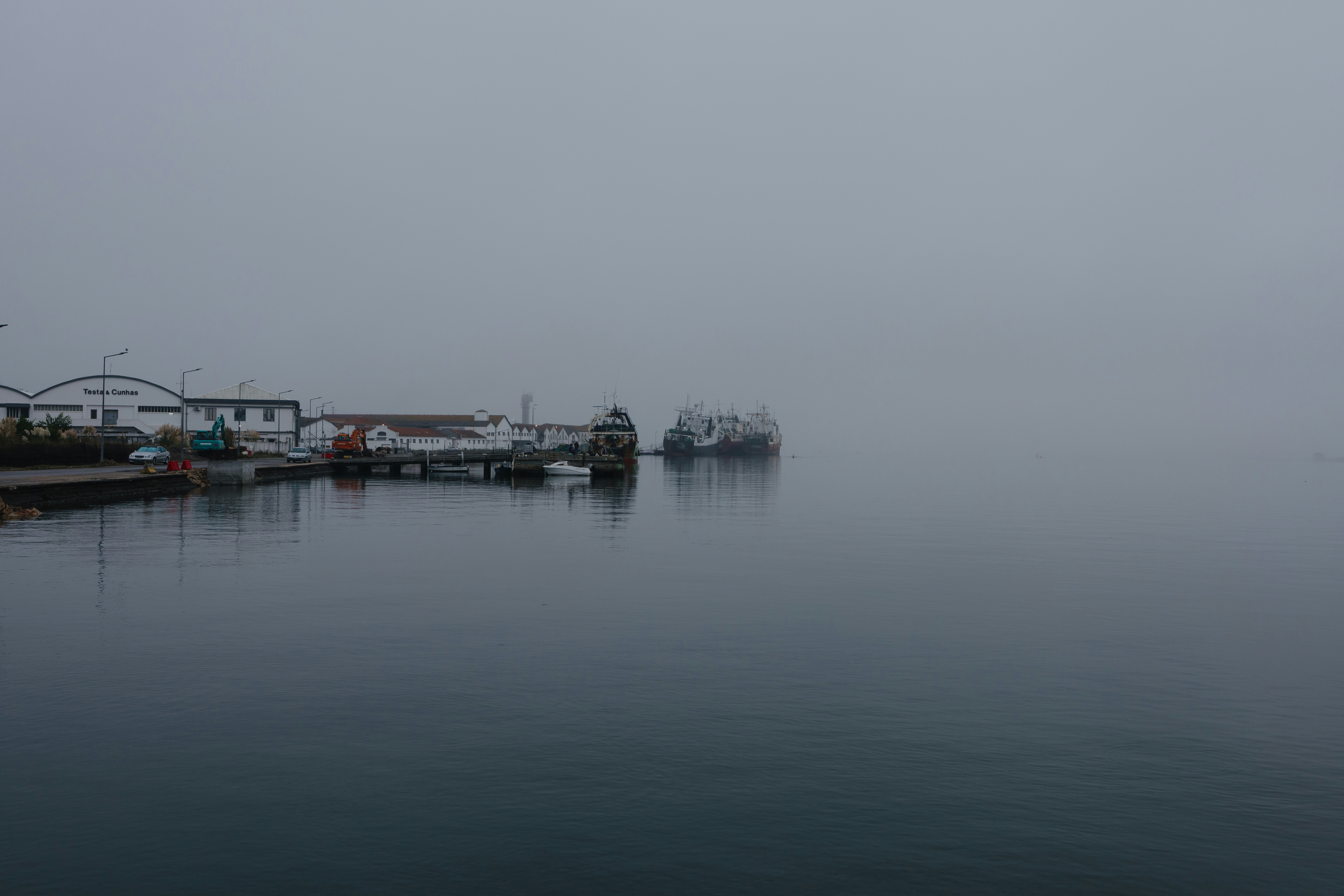 Foggy harbor scene with boats anchored near a quiet waterfront, evoking a sense of tranquility and solitude.