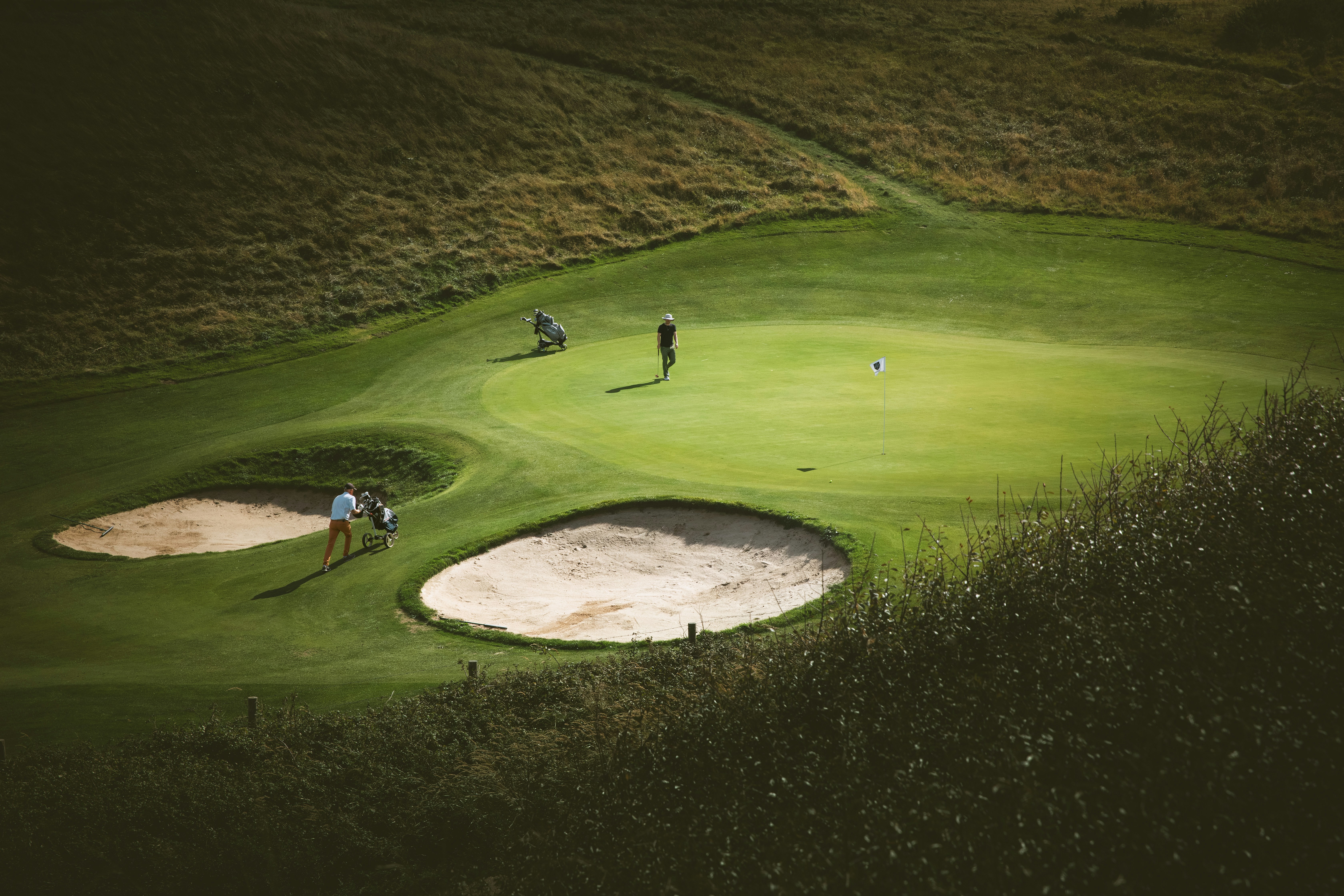 Golfers on a green with sand traps and rough grass.