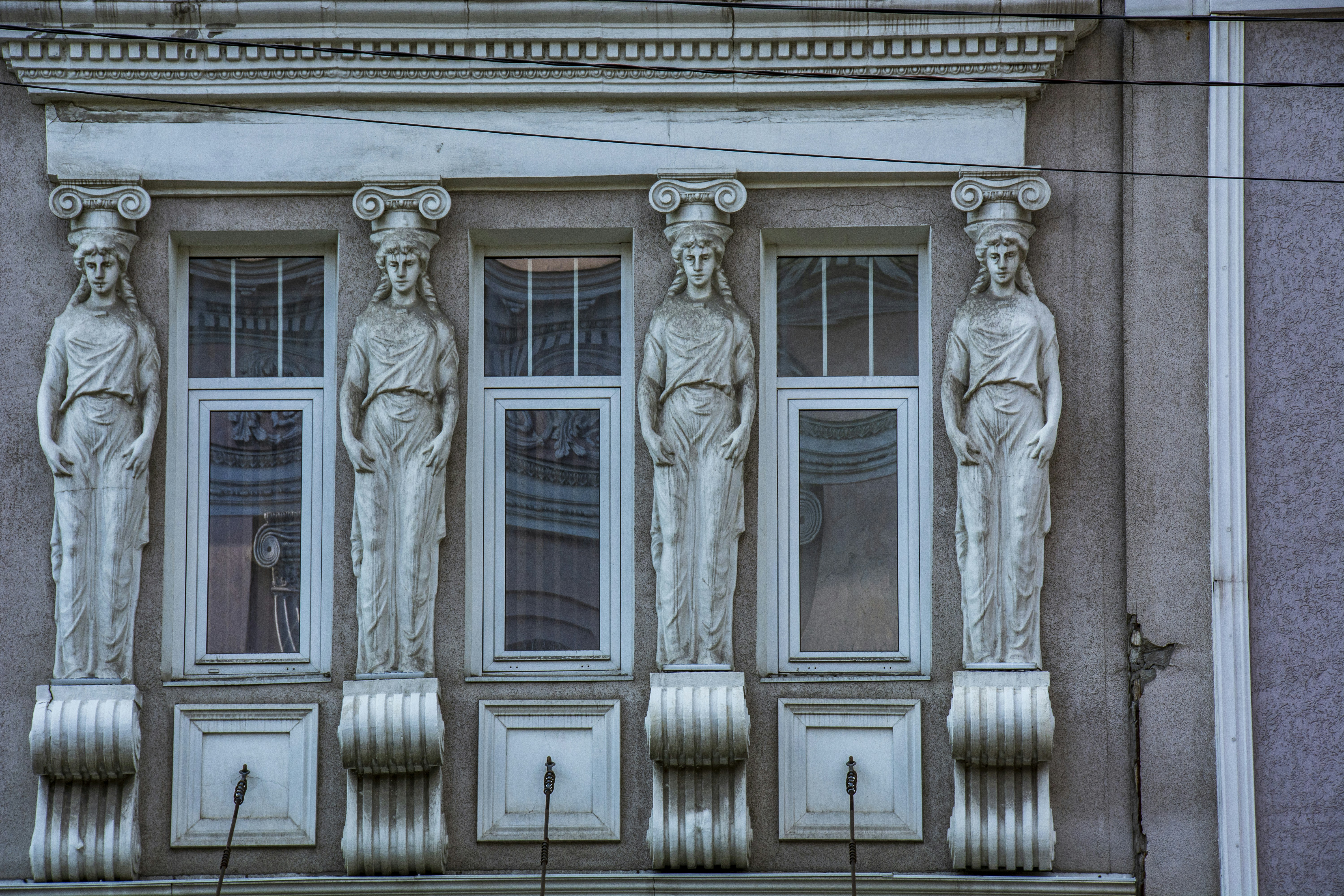Five classical statues adorn windows on a building.