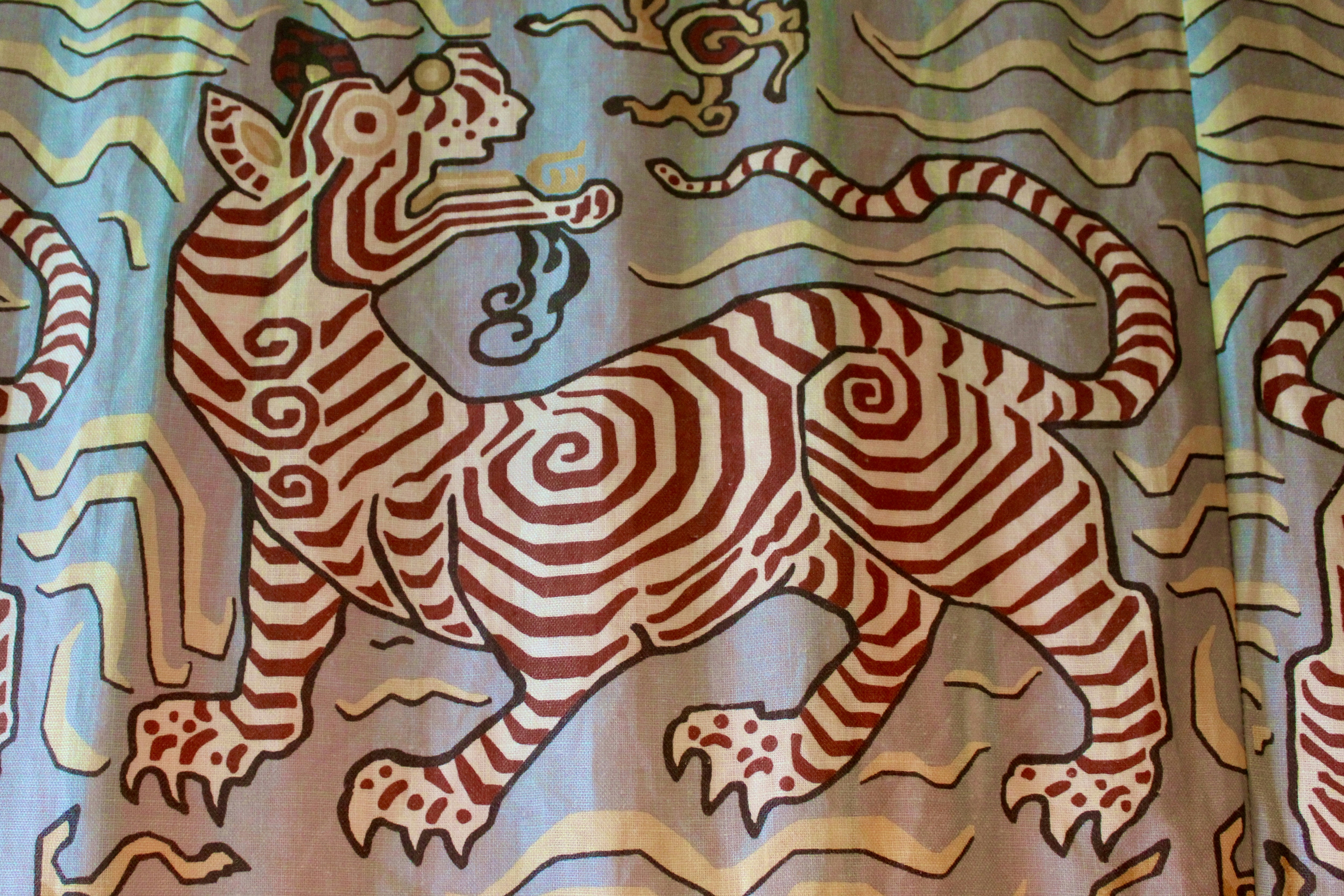 A stylized tiger adorned with swirling red and white patterns, set against a soft blue backdrop. The illustration captures a blend of cultural artistry and imaginative design.