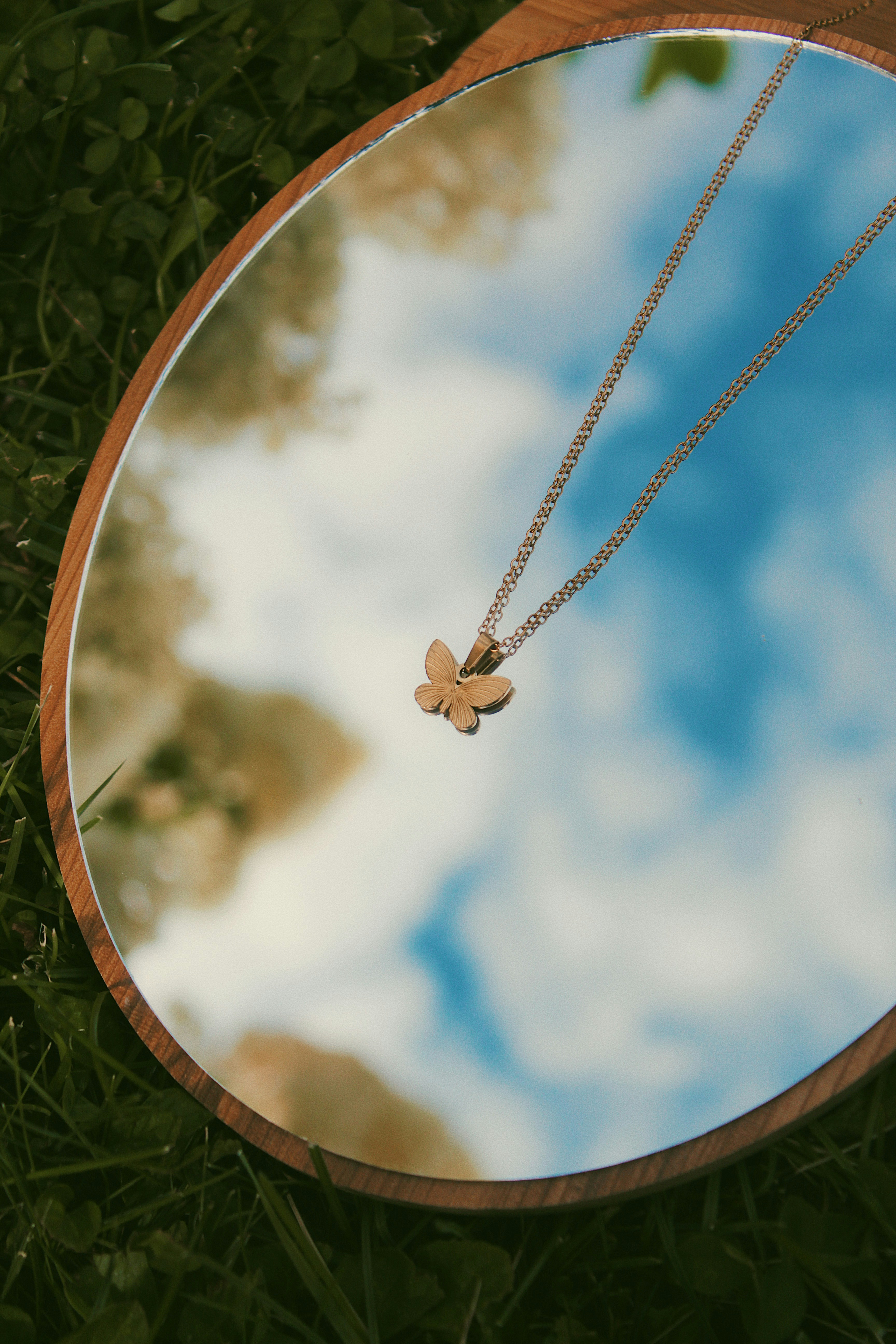 Butterfly necklace reflected in mirror with sky.