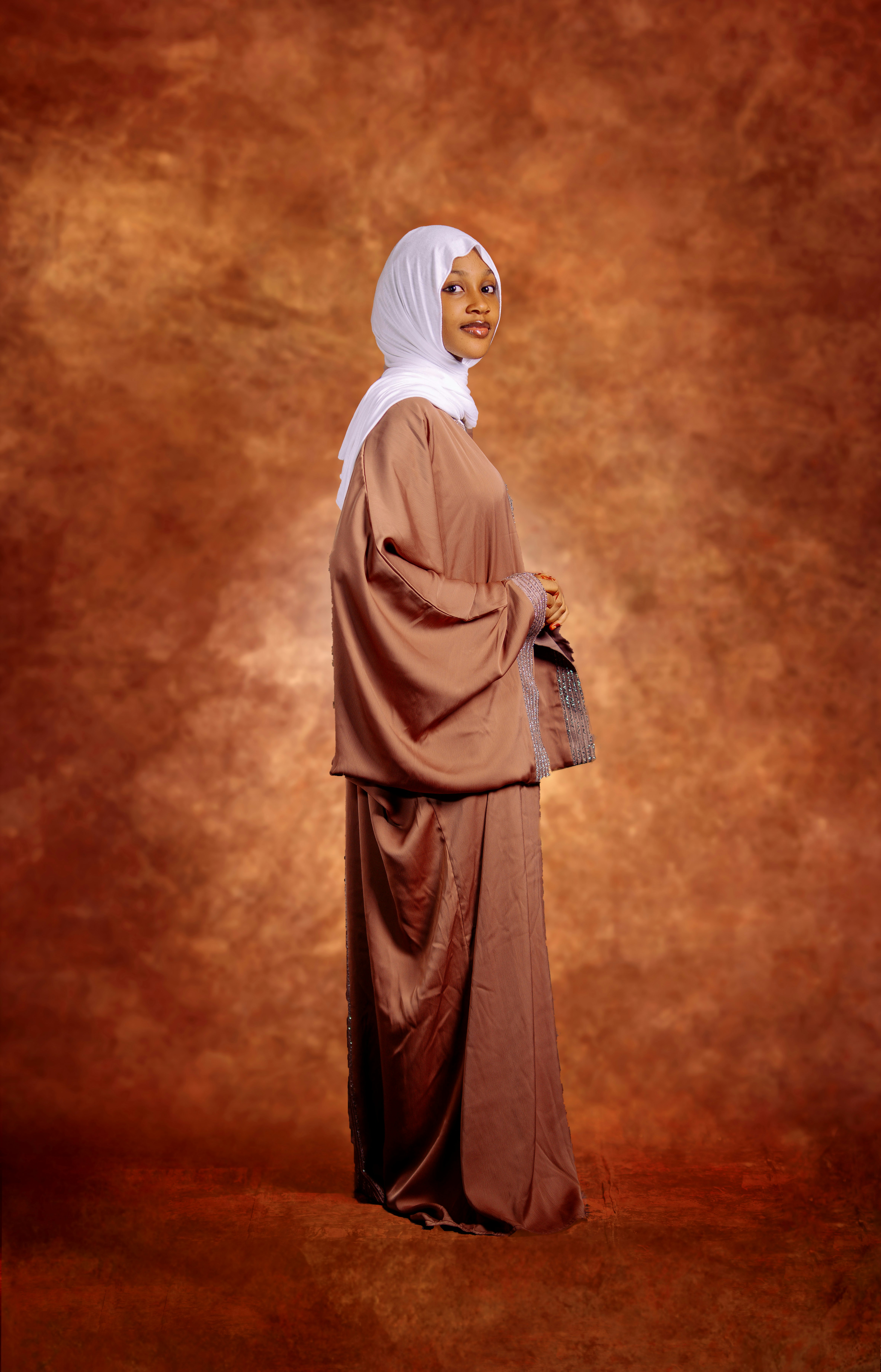 A woman in a brown hijab and dress smiles.