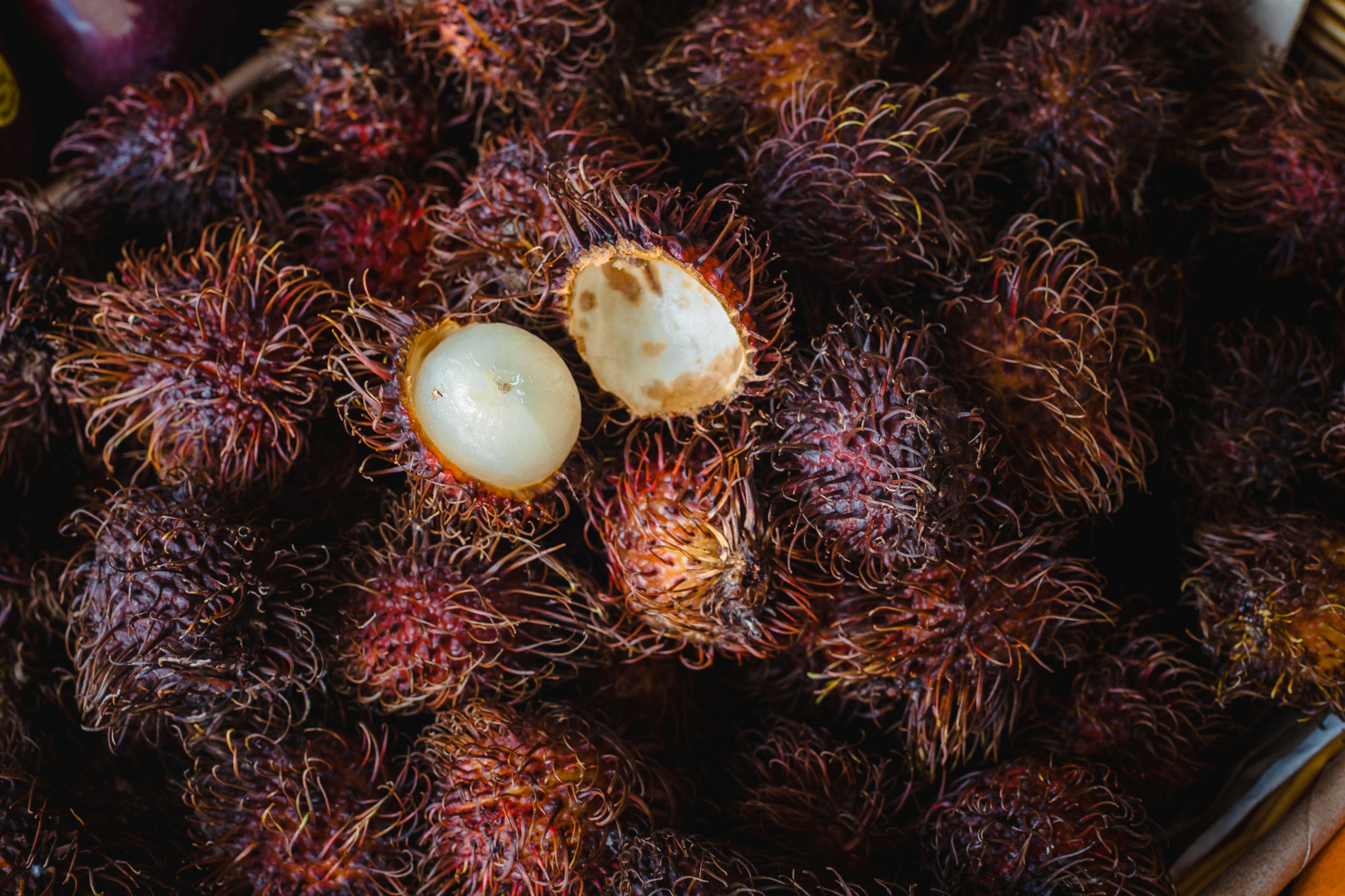 A cluster of rambutan fruits with one fruit partially peeled, revealing its translucent flesh. The vibrant colors and unique textures highlight the exotic appeal of this tropical delicacy.
