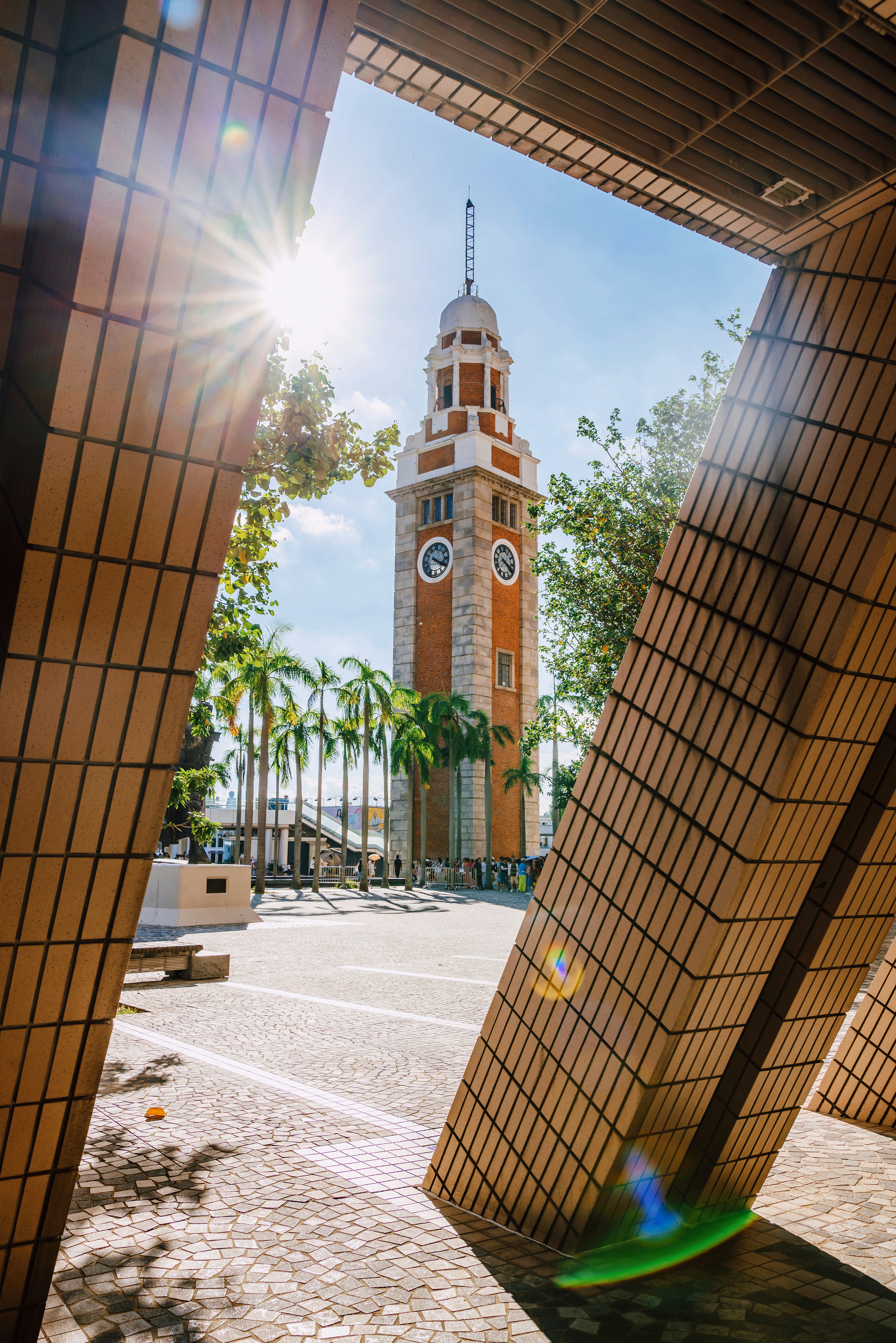 Historic clock tower framed by modern architectural elements, with sunlight streaming through the structure. 