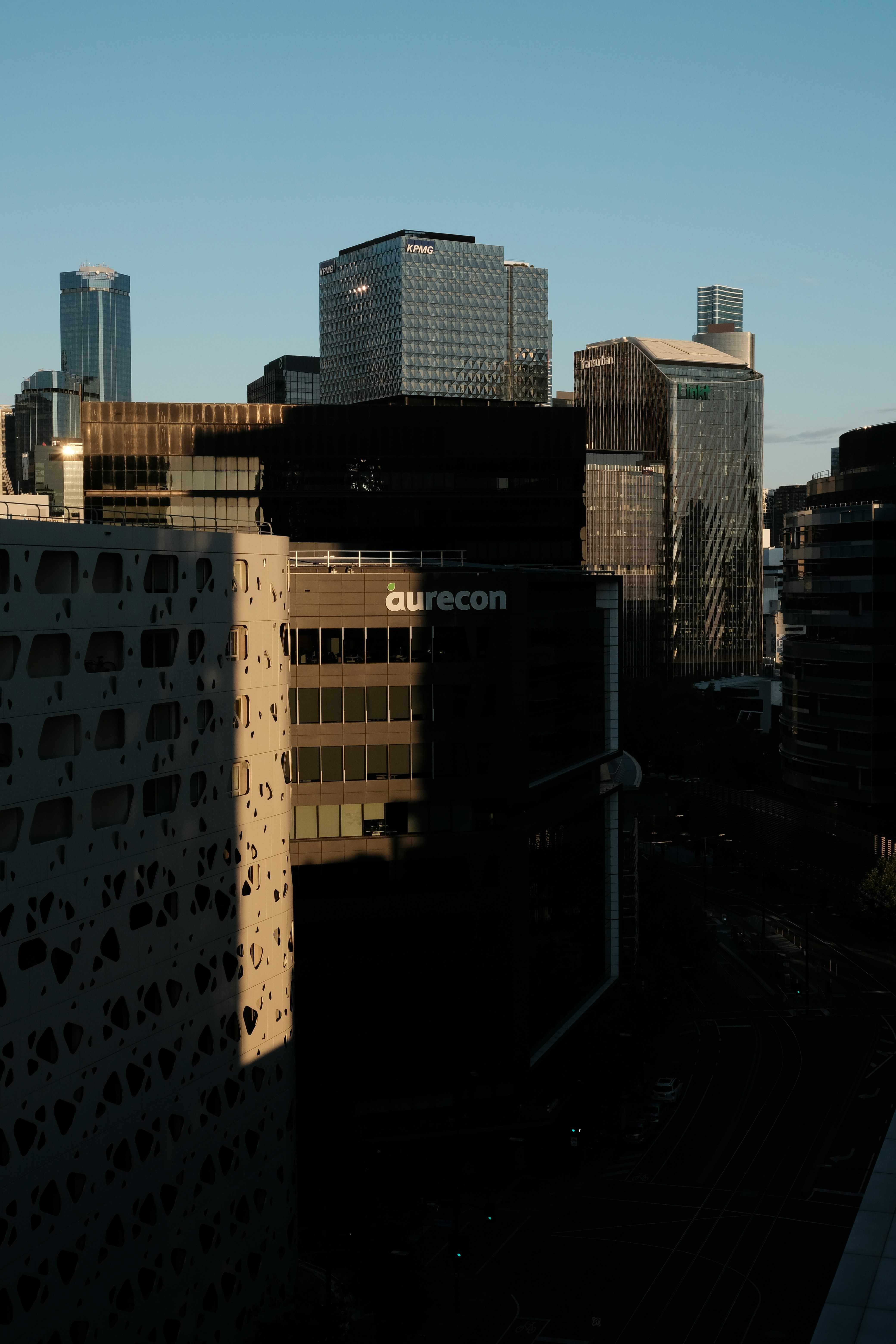 Modern skyscrapers reflecting the evening light, framed by the shadow of a nearby building. The scene captures the interplay of light and architecture.