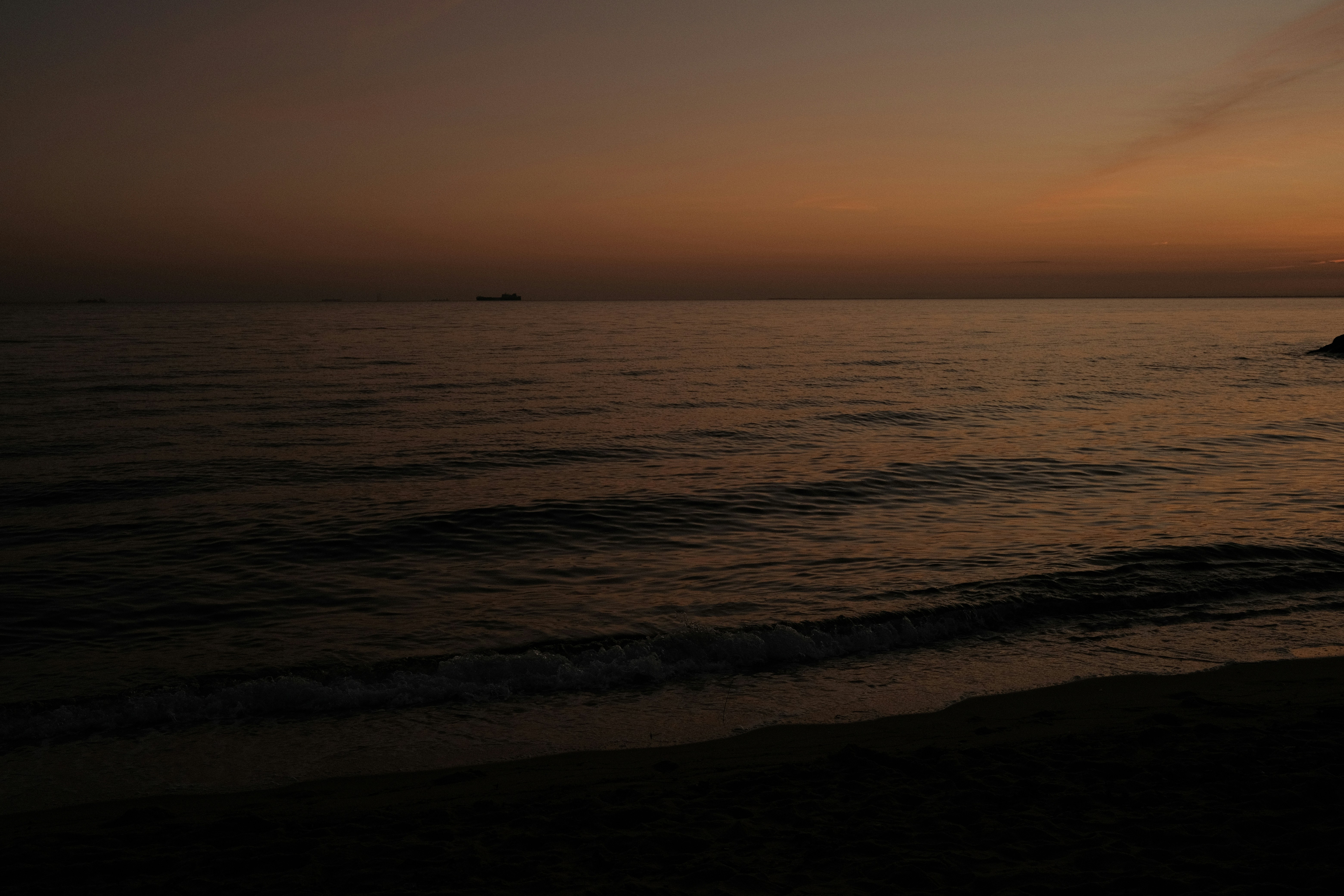 Calm ocean waves at dusk with a distant ship.