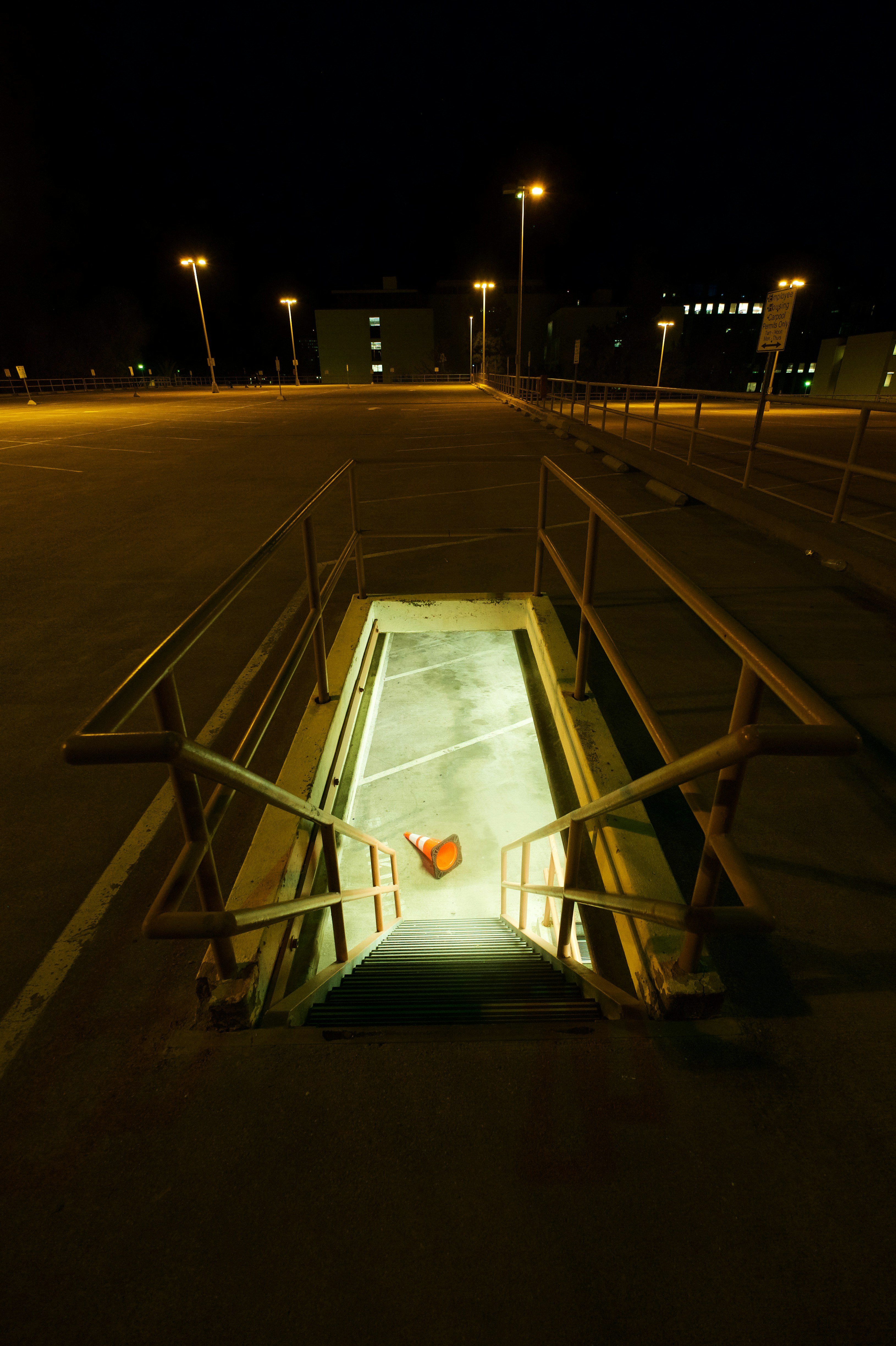 going down the stairs you see a cone | Stairwell entrance in a dimly lit parking lot at night.