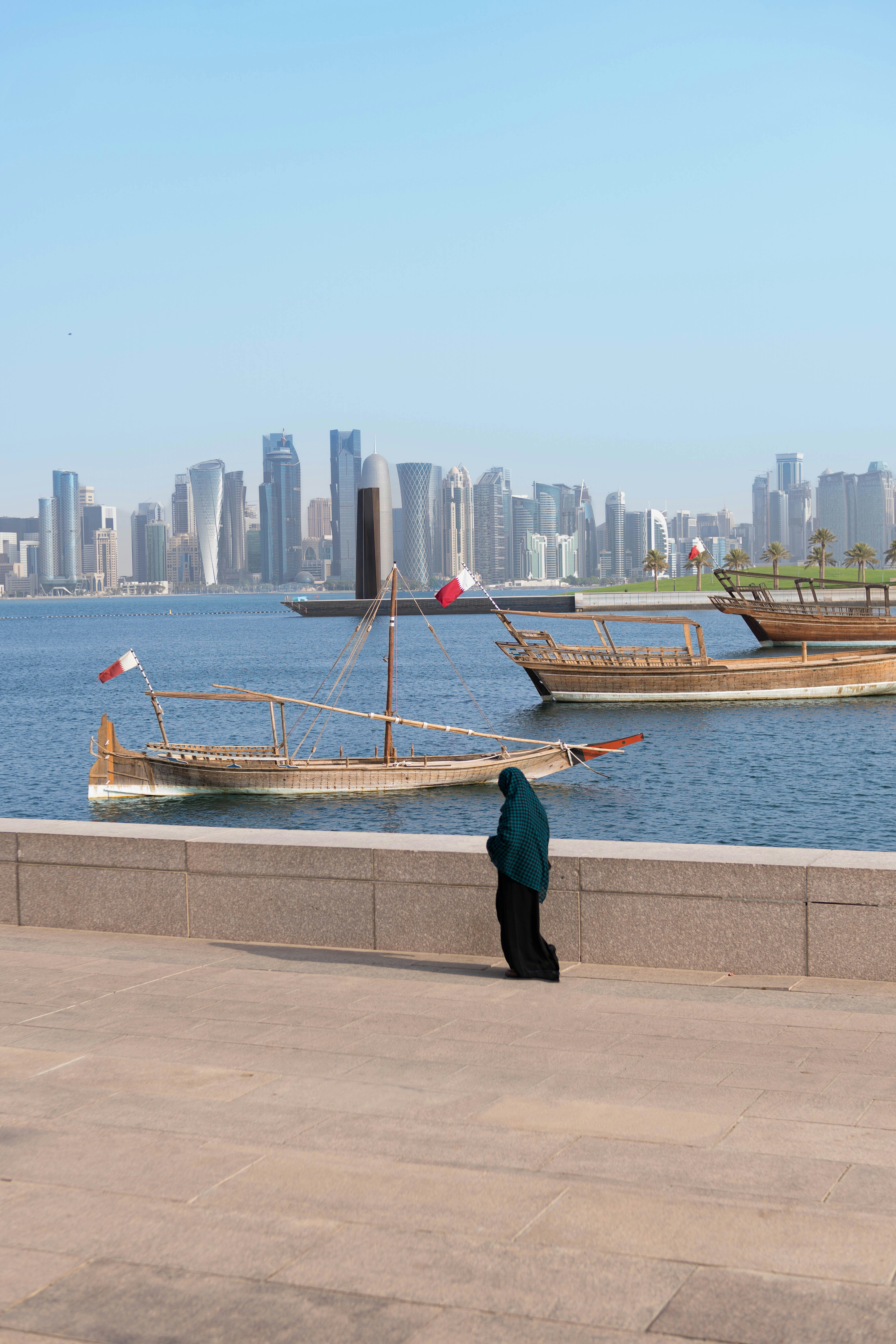 Harbor Gaze: A lone figure by weathered boats against a skyline of glass towers