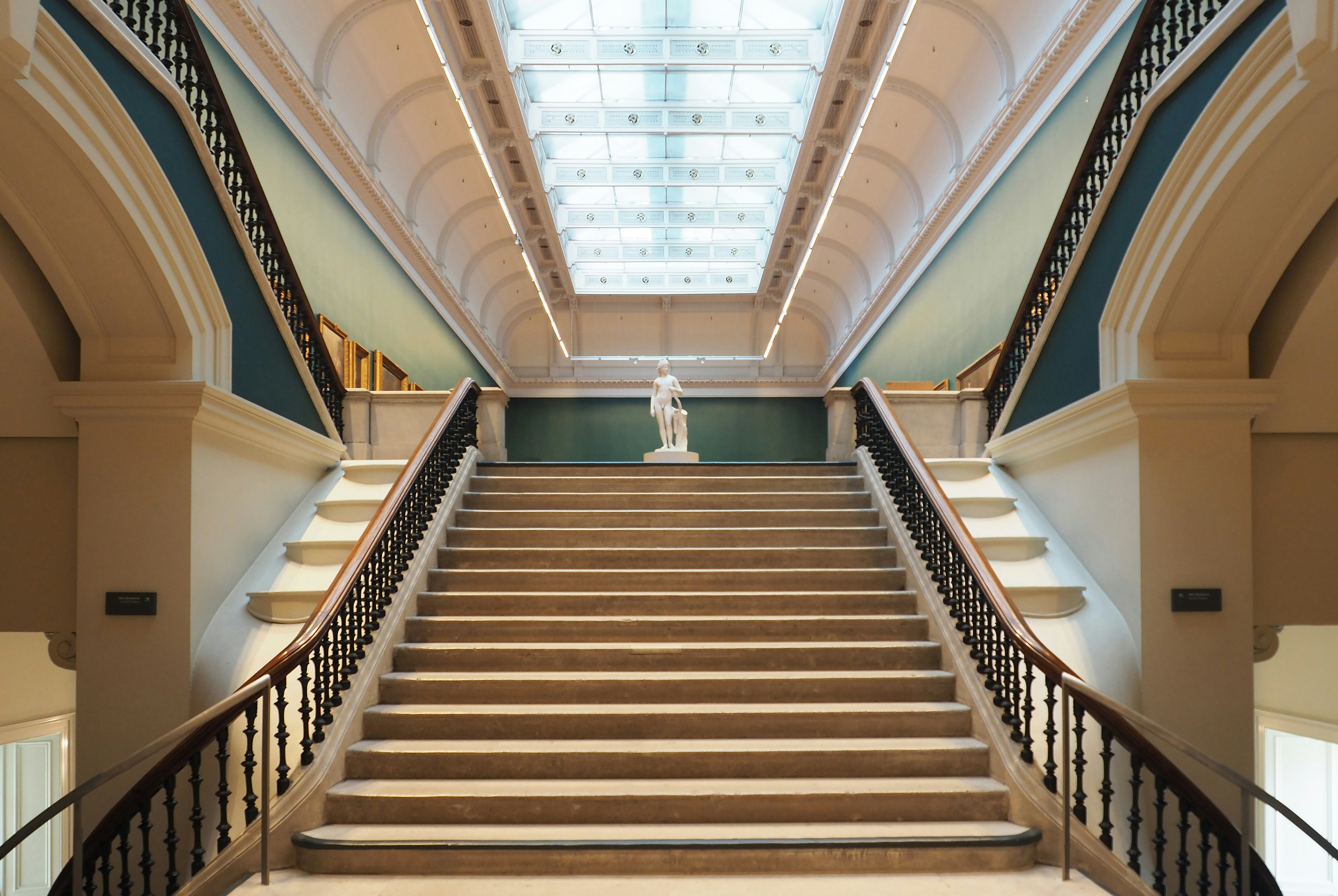 Grand staircase leading to a statue, framed by intricate railings and a skylight above. The design highlights the harmony of space and light.