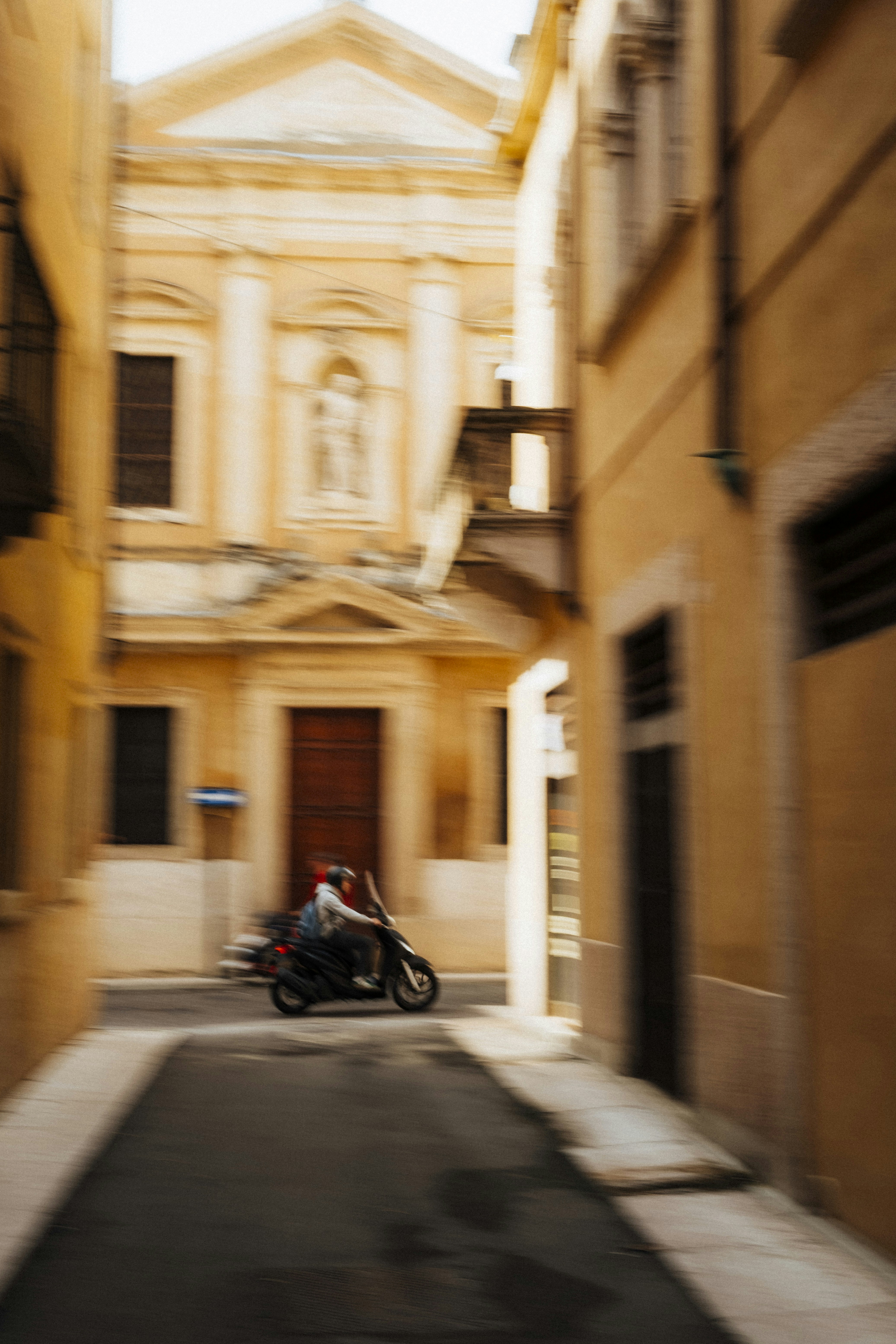 Motorcyclist rides down a narrow european street.