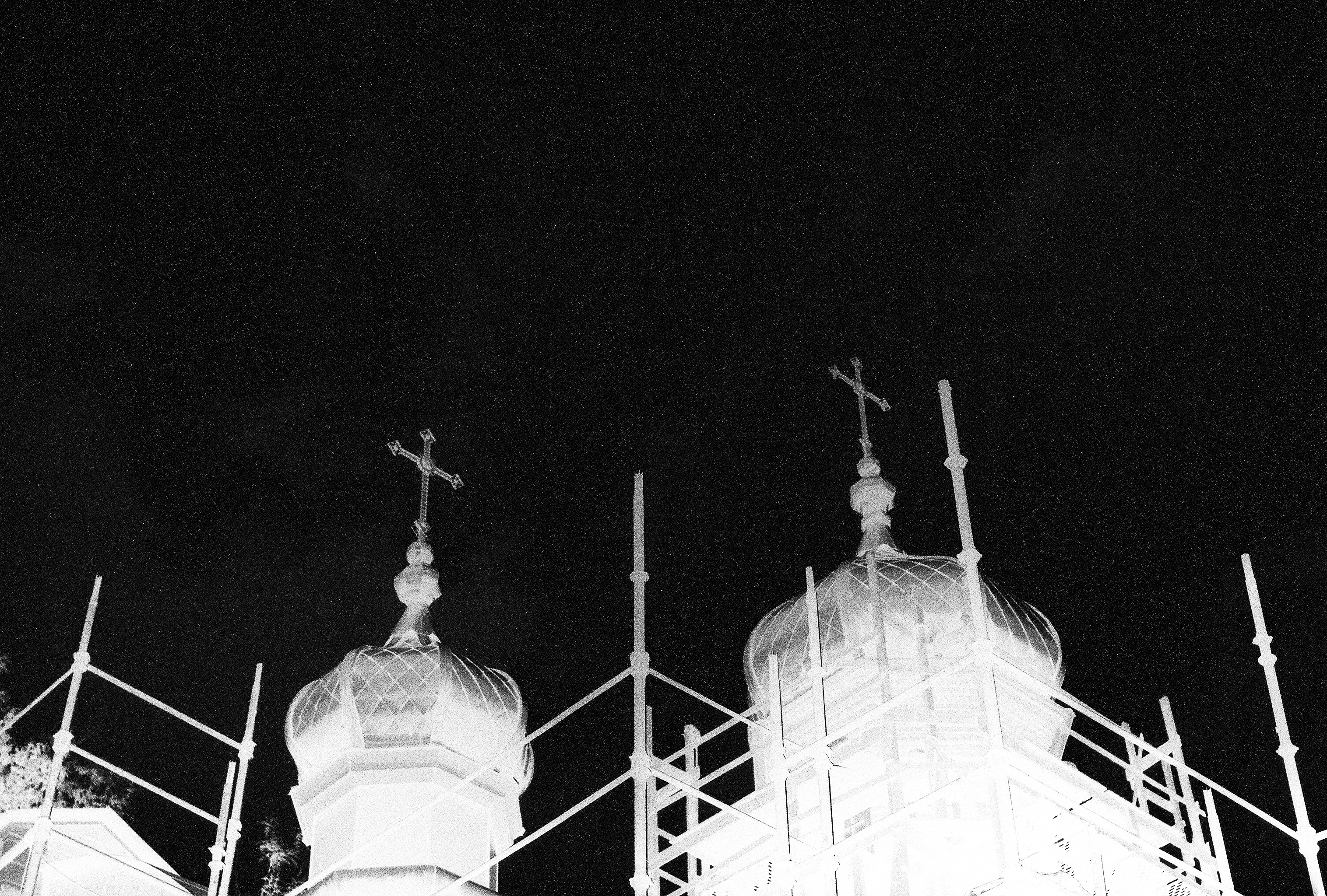 Two domes with crosses silhouetted against a dark sky, surrounded by scaffolding, hinting at ongoing restoration work.