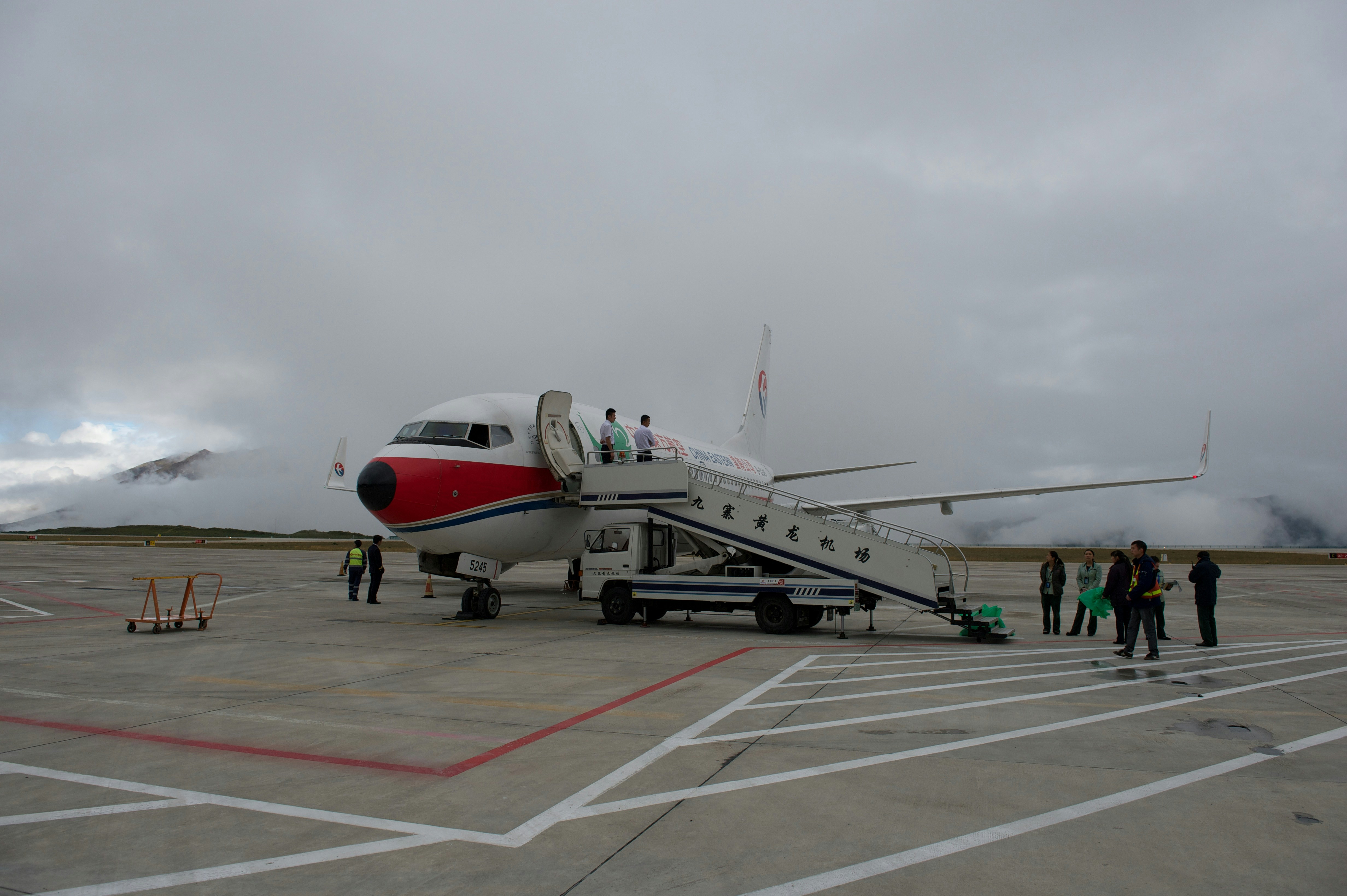 Passenger disembarking from a Chinese airplane against misty mountain | Airplane with boarding stairs and passengers on tarmac.