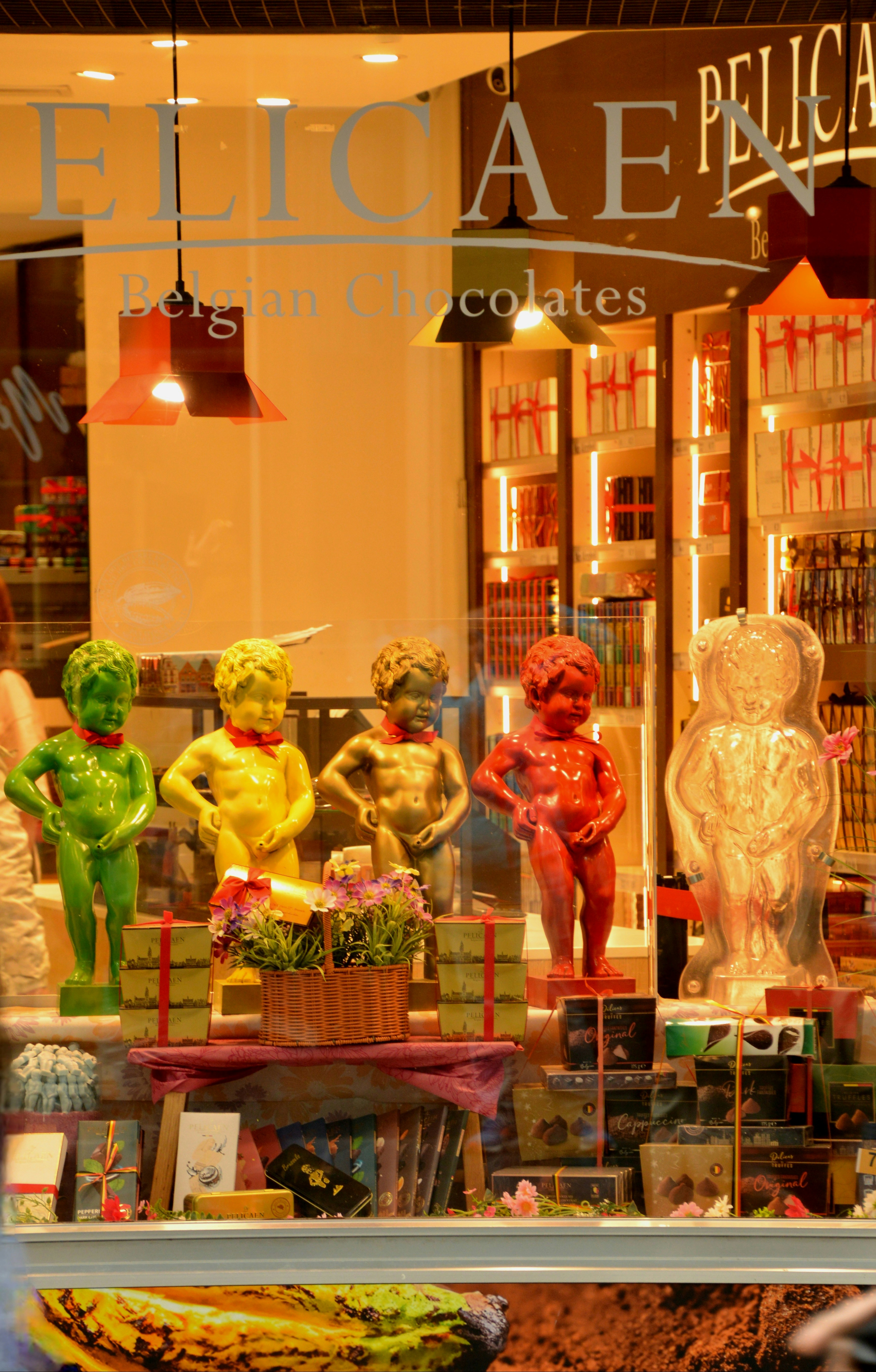 Colorful chocolate sculptures inspired by Manneken Pis displayed in a Belgian chocolate shop window in Brussels. A vibrant glimpse of Belgian culture and sweets. | Chocolate shop window display with manneken pis statues