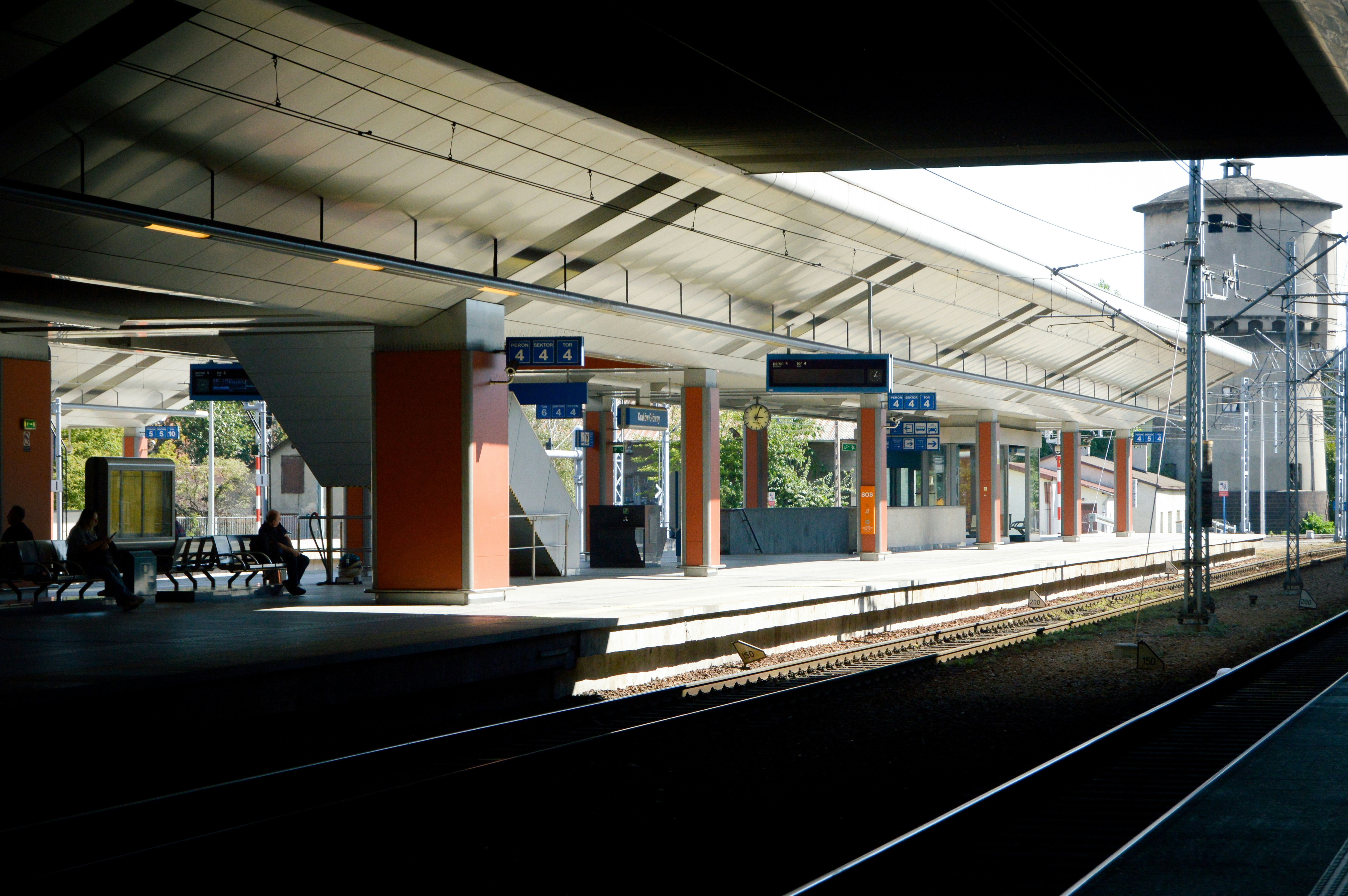 Modern train station platform showcasing architectural design and passenger seating, with tracks leading into the distance.