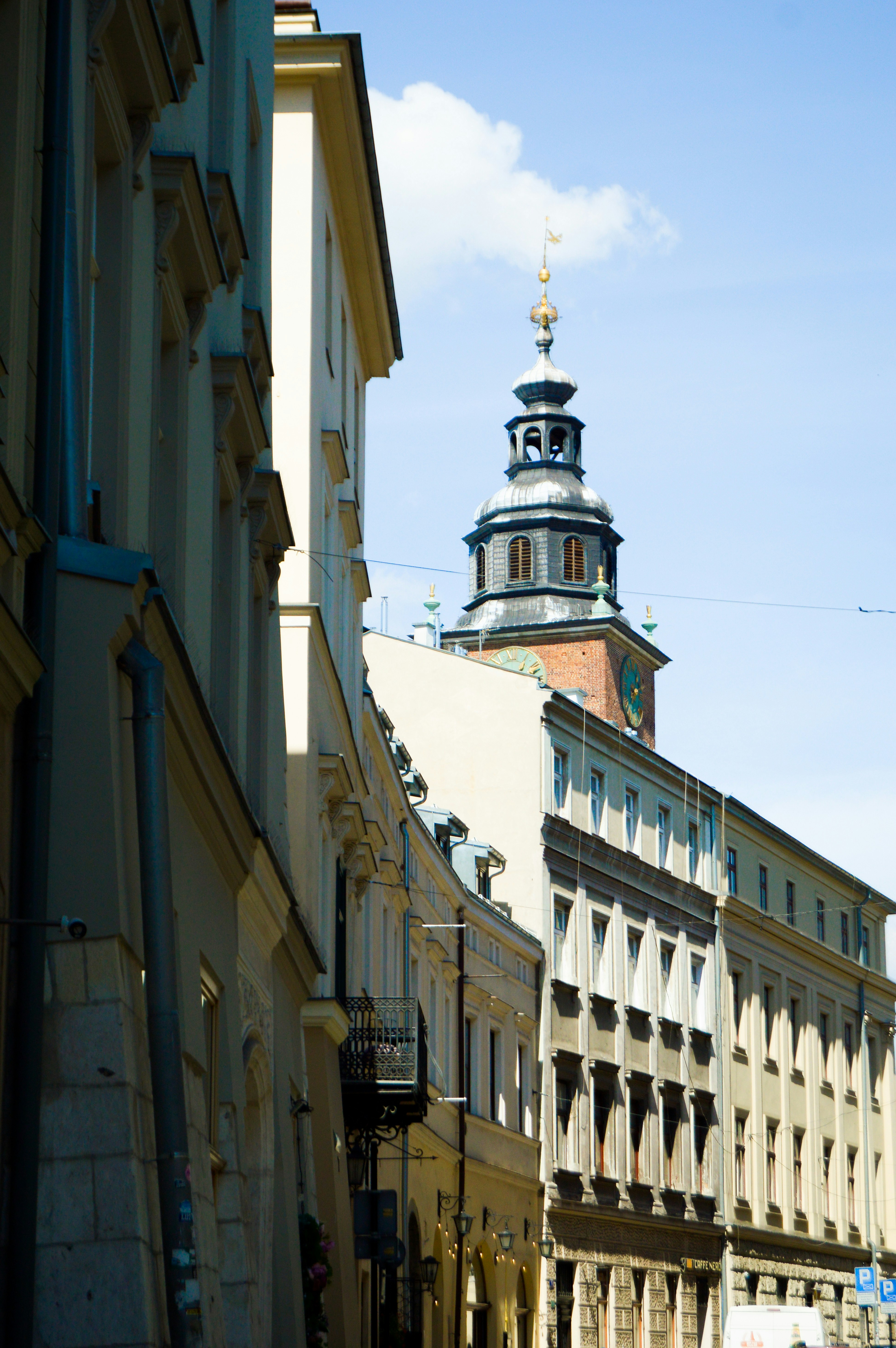 Historic architecture lines a narrow street, leading the eye to a prominent clock tower against a clear blue sky.