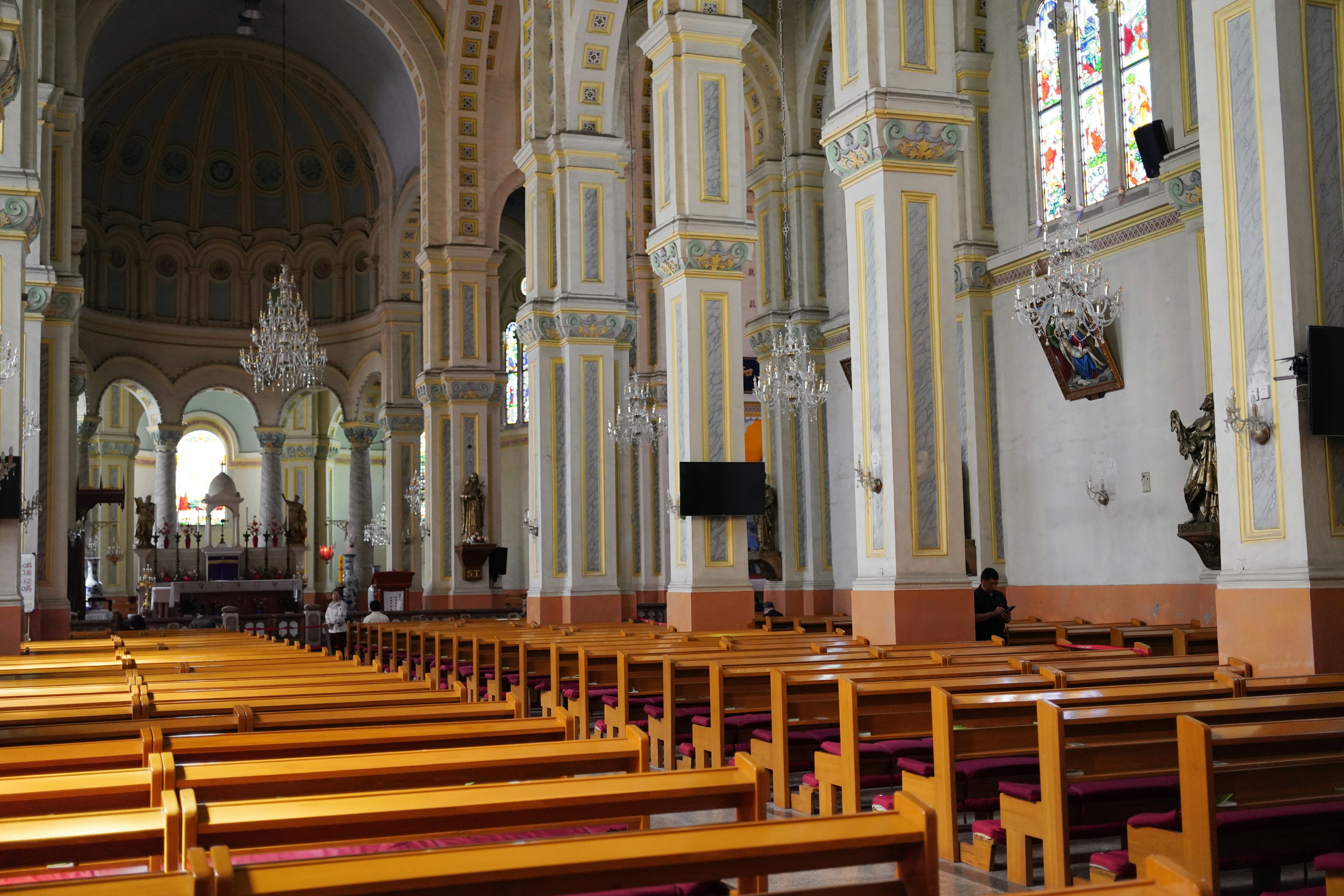 Interior of a grand church showcasing intricate architecture and rows of wooden pews, illuminated by stained glass windows. The serene atmosphere invites reflection.