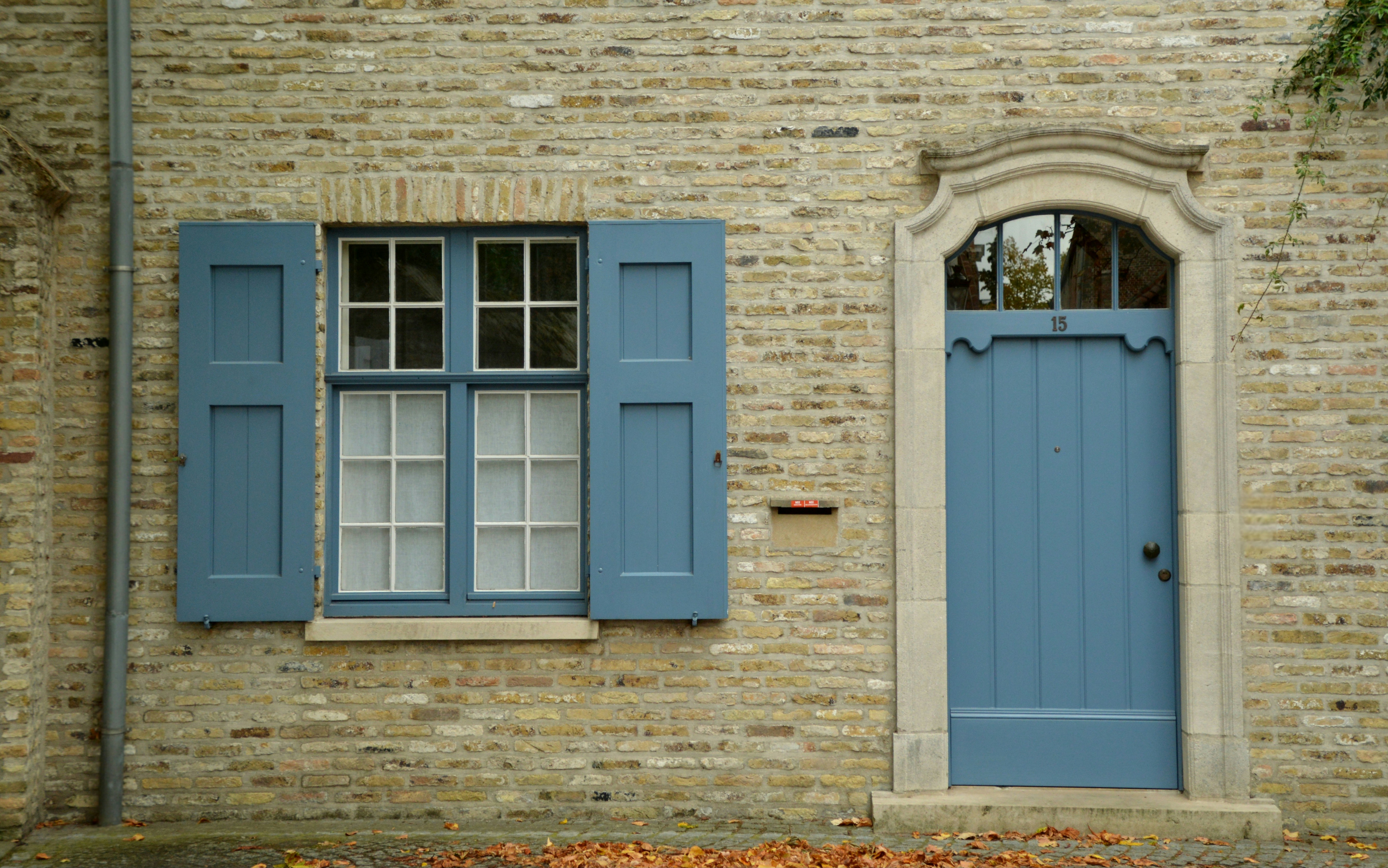 Minimalist view of a brick wall with a window and door of a traditional European house | Blue door and shutters on brick building