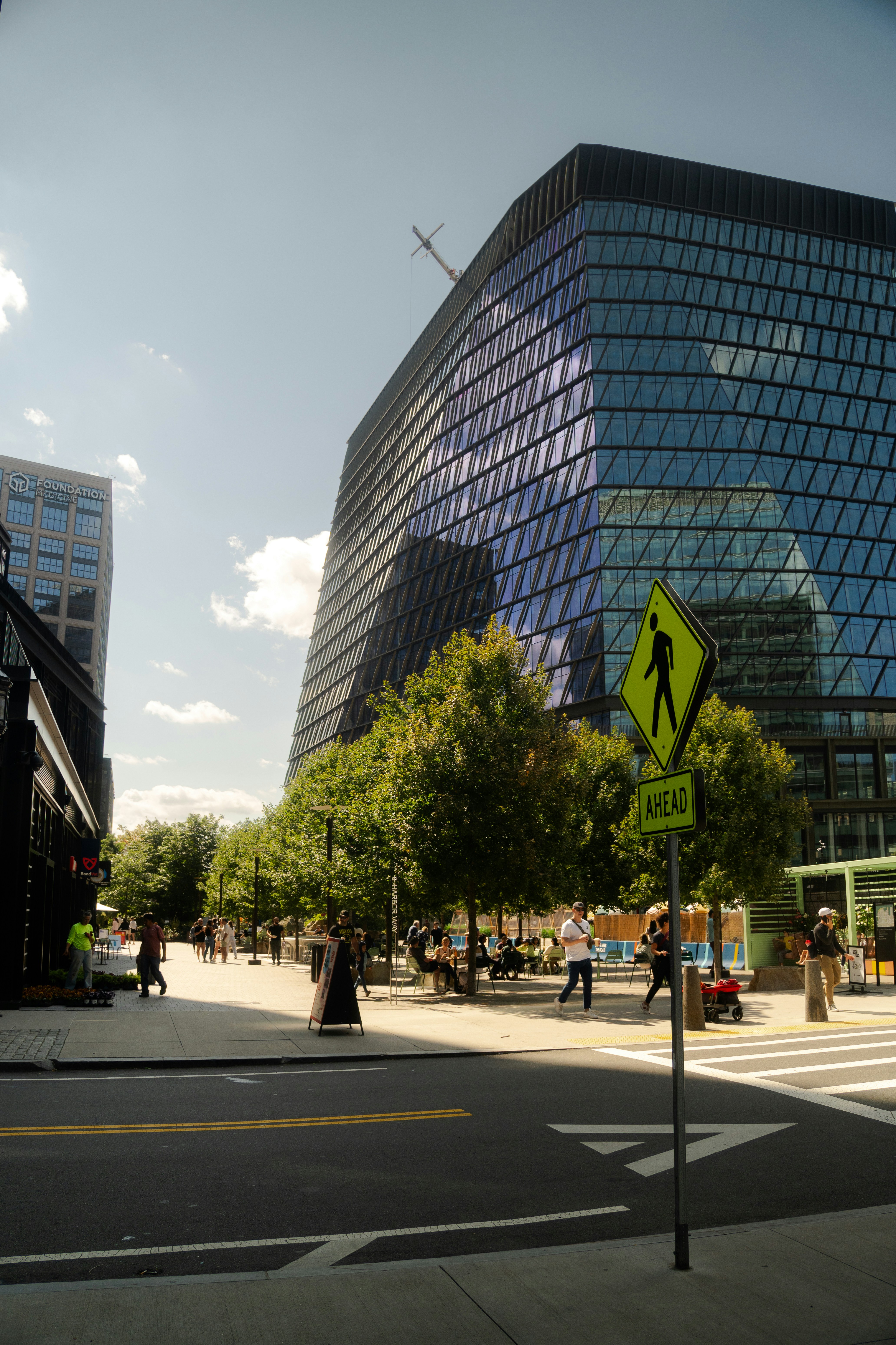 Modern glass building with trees and people walking.