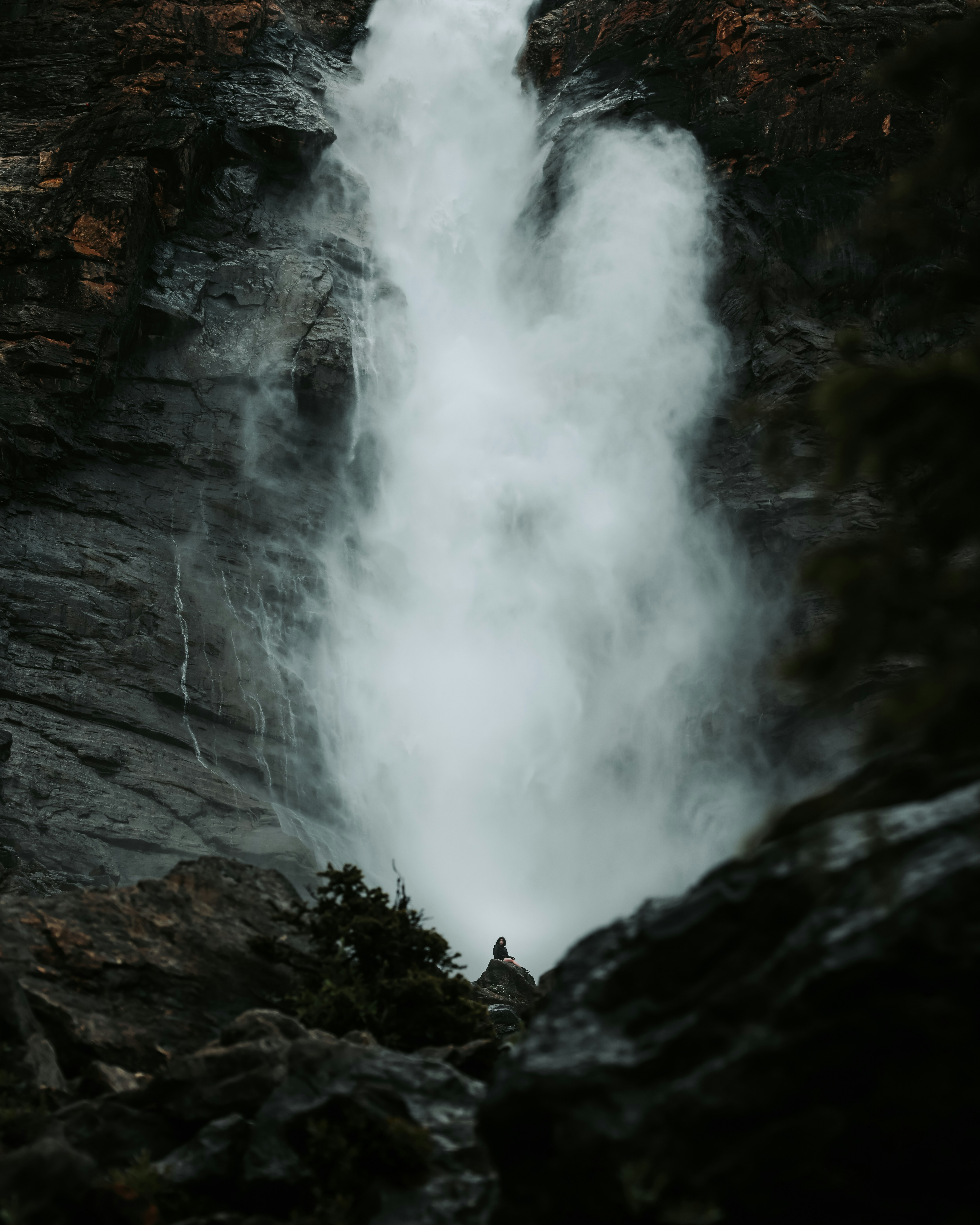 A person stands before a powerful waterfall cascading down rocks.