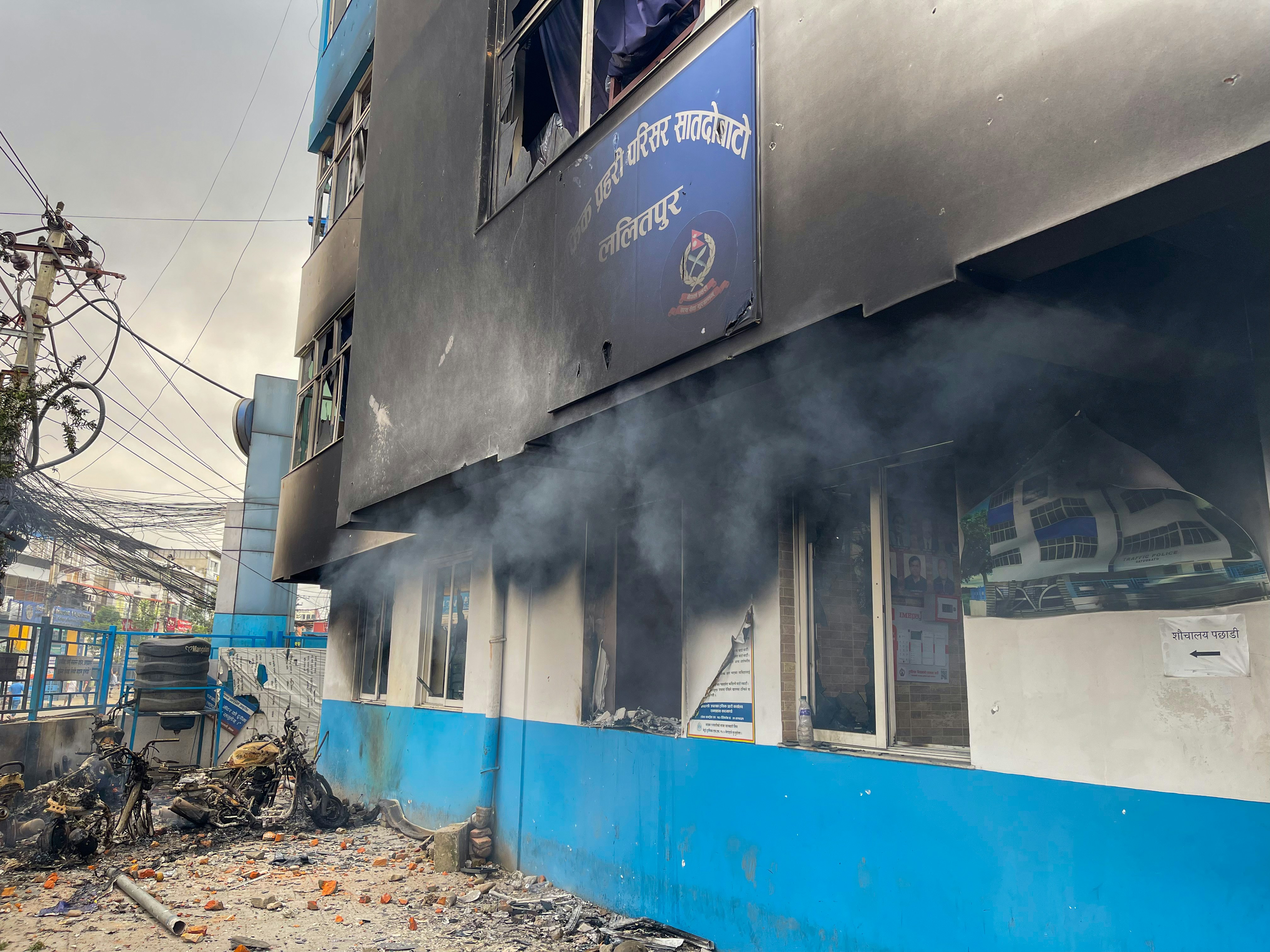 Burning police office with smoke Description: A Nepal Police office in Lalitpur shows heavy fire damage, with smoke billowing from broken windows during the September 9 protest. The attack on government property represents a peak in the intensity of the demonstration. | Building with smoke billowing from windows