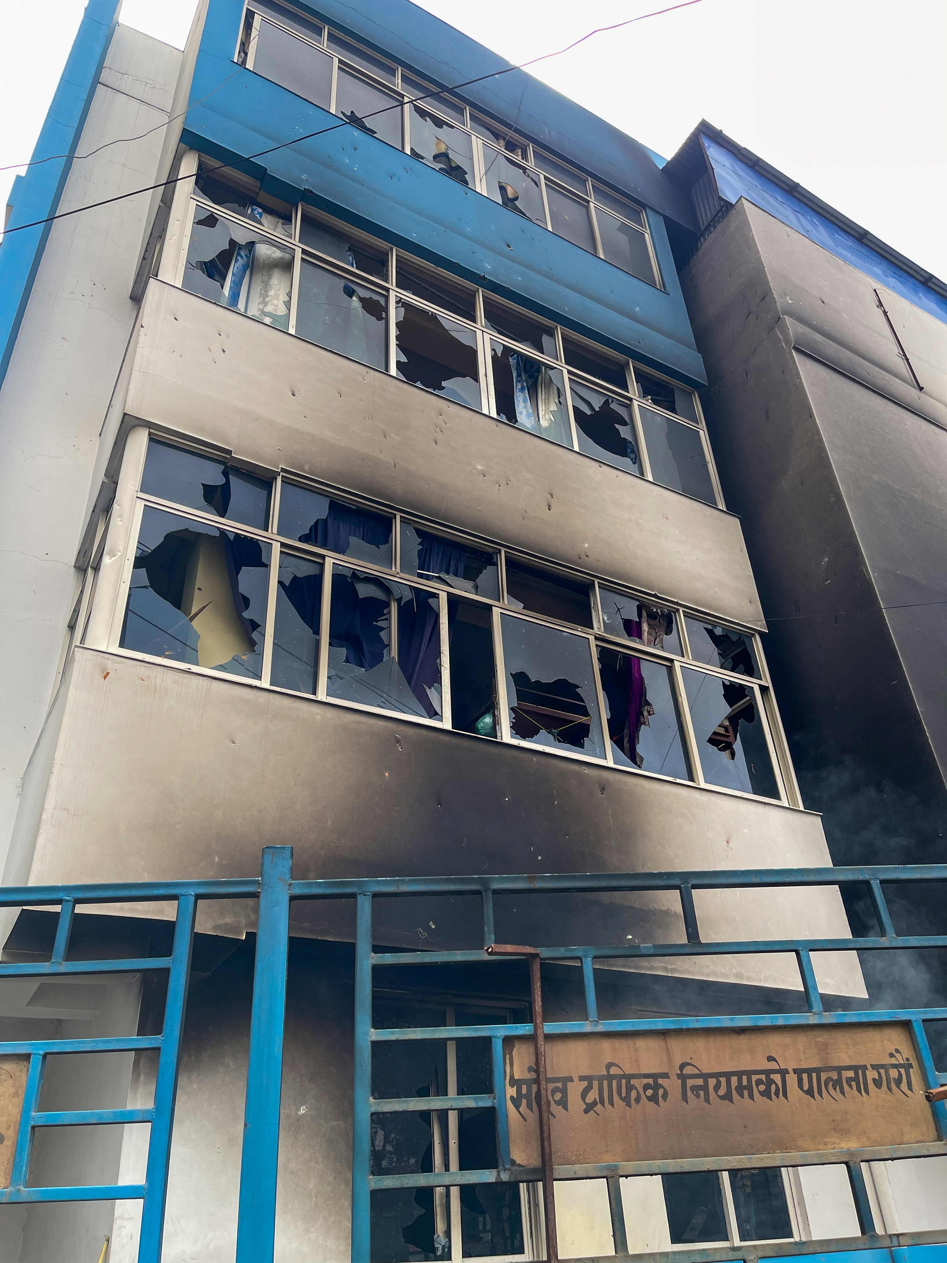 Burnt and damaged building with broken windows A building heavily damaged during the Nepal protest shows broken windows, soot marks, and signs of fire. The structure stands as evidence of violent clashes, reflecting anger and destruction in the heart of the city. | Building with shattered windows and smoke damage