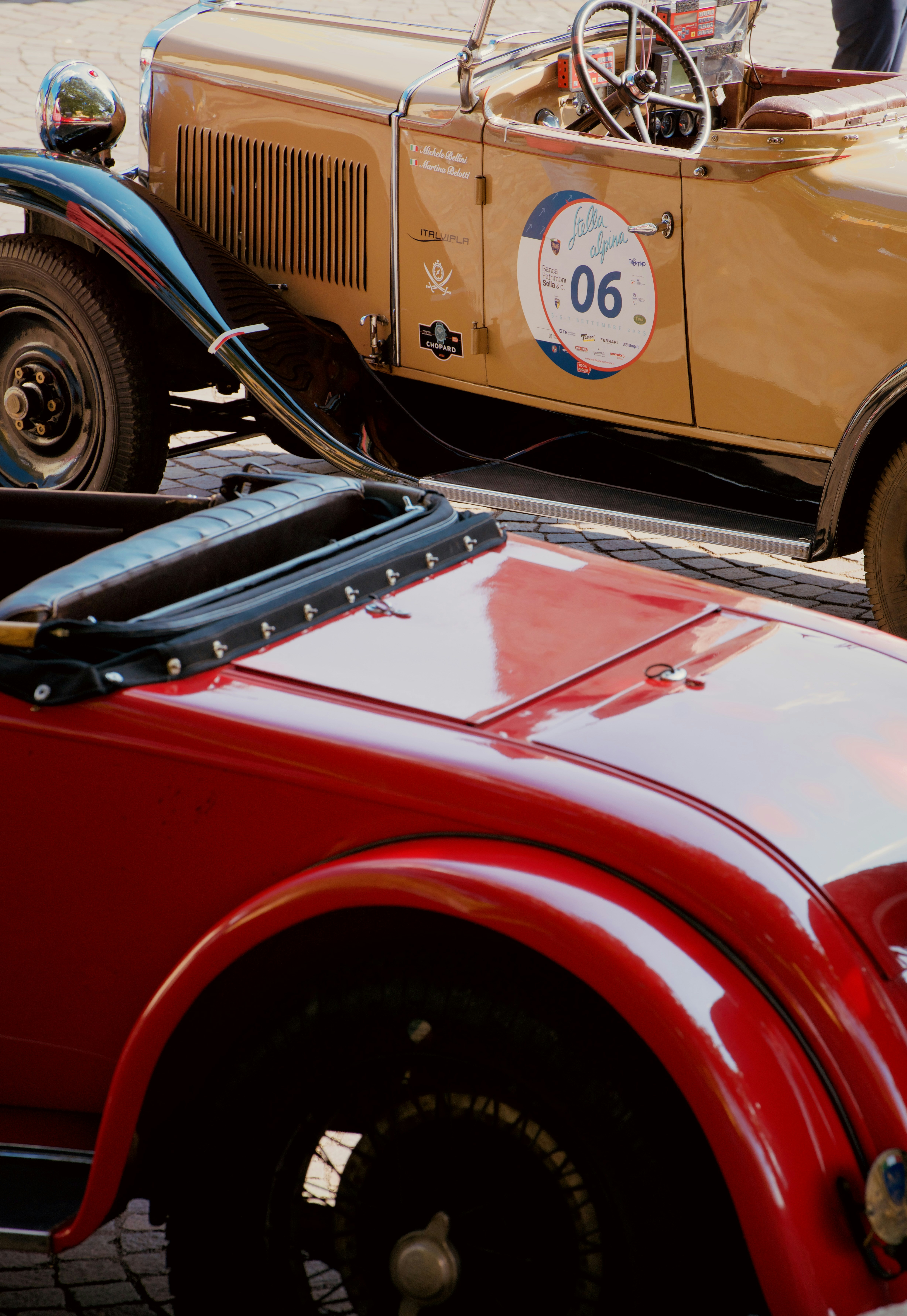 Two classic cars in vibrant colors showcase their timeless design at a vintage car event.