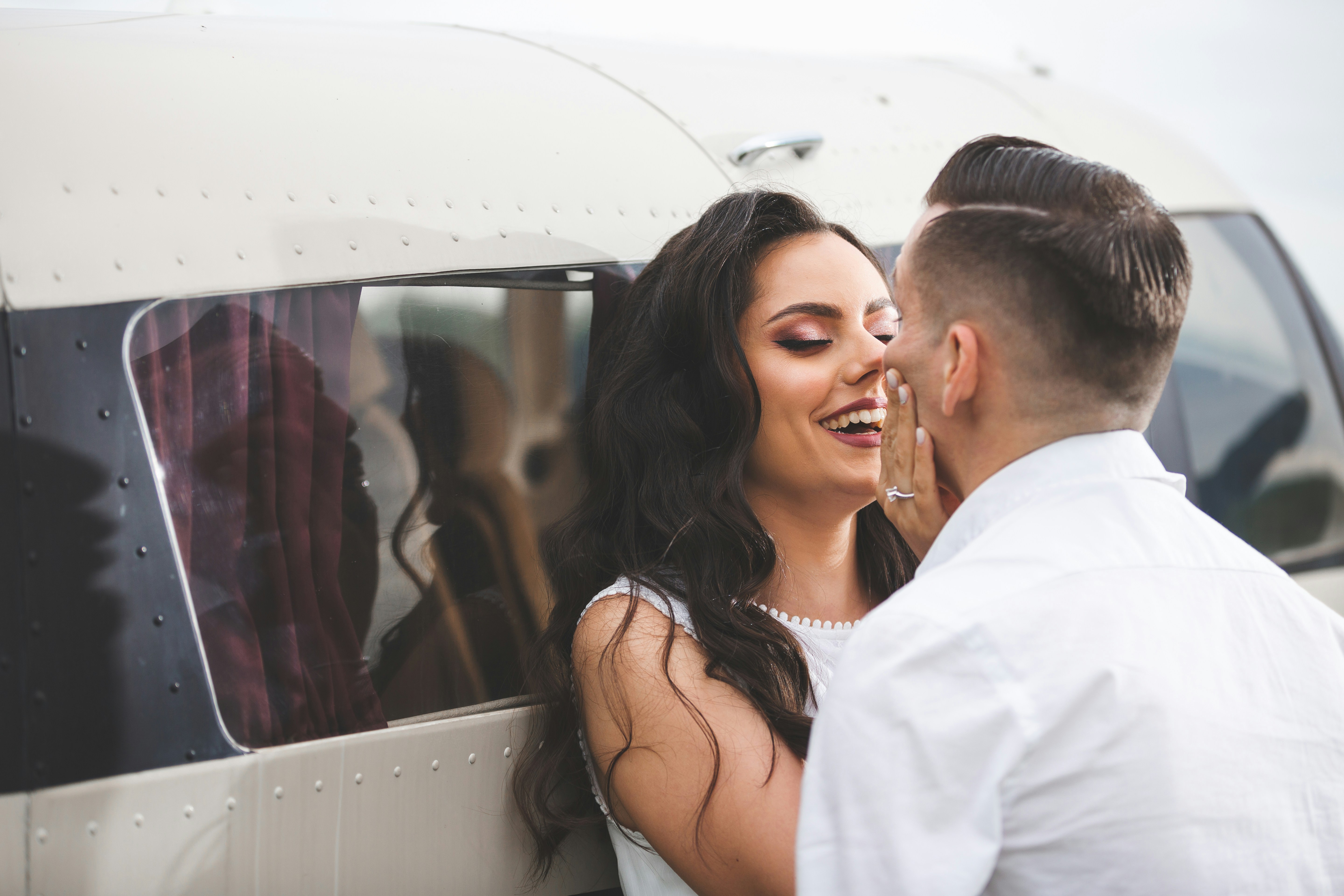 Couple sharing a playful moment by a vintage airplane, showcasing their affection and connection. The scene captures the essence of love and adventure.