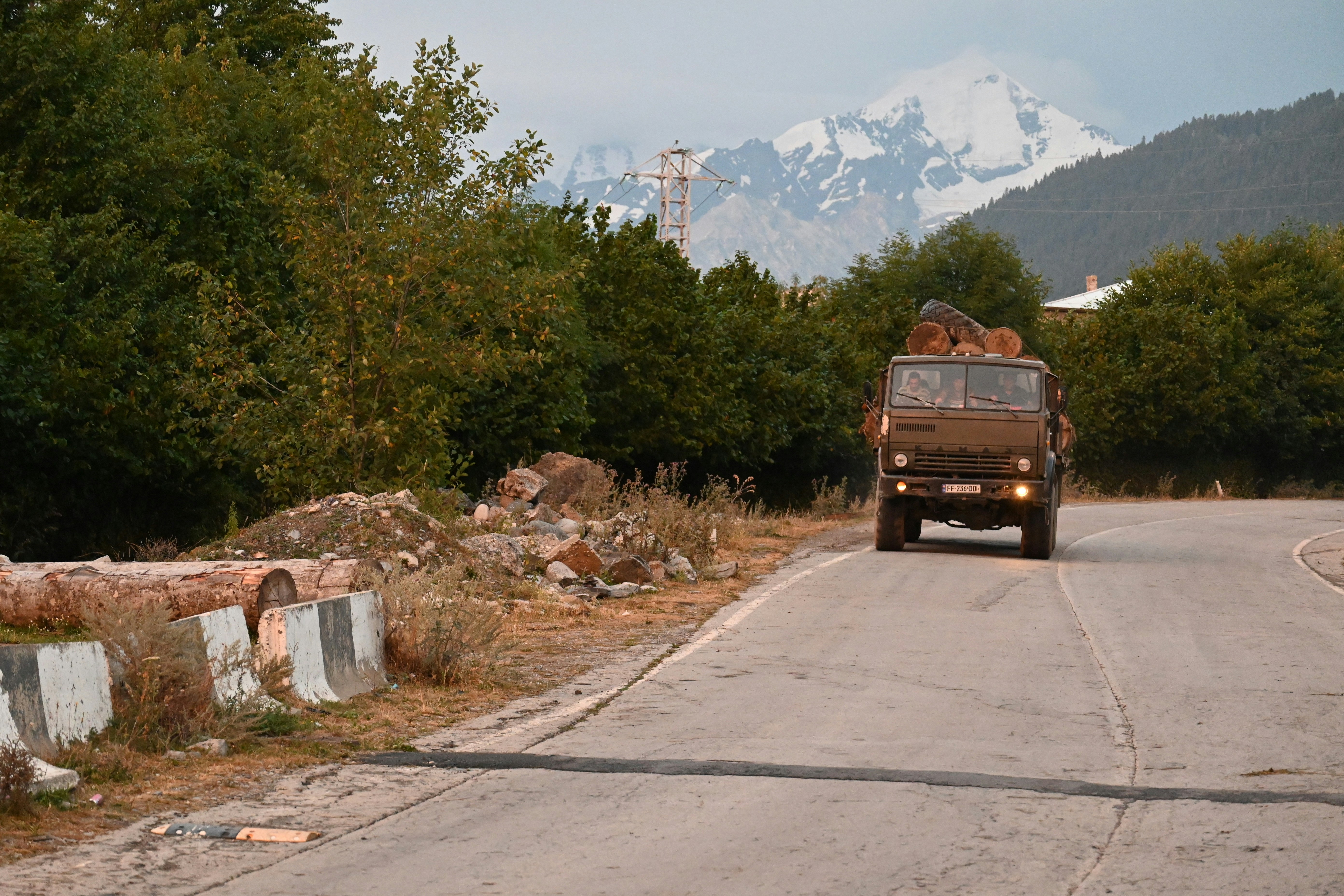 Truck carrying logs on a winding road with mountains.
