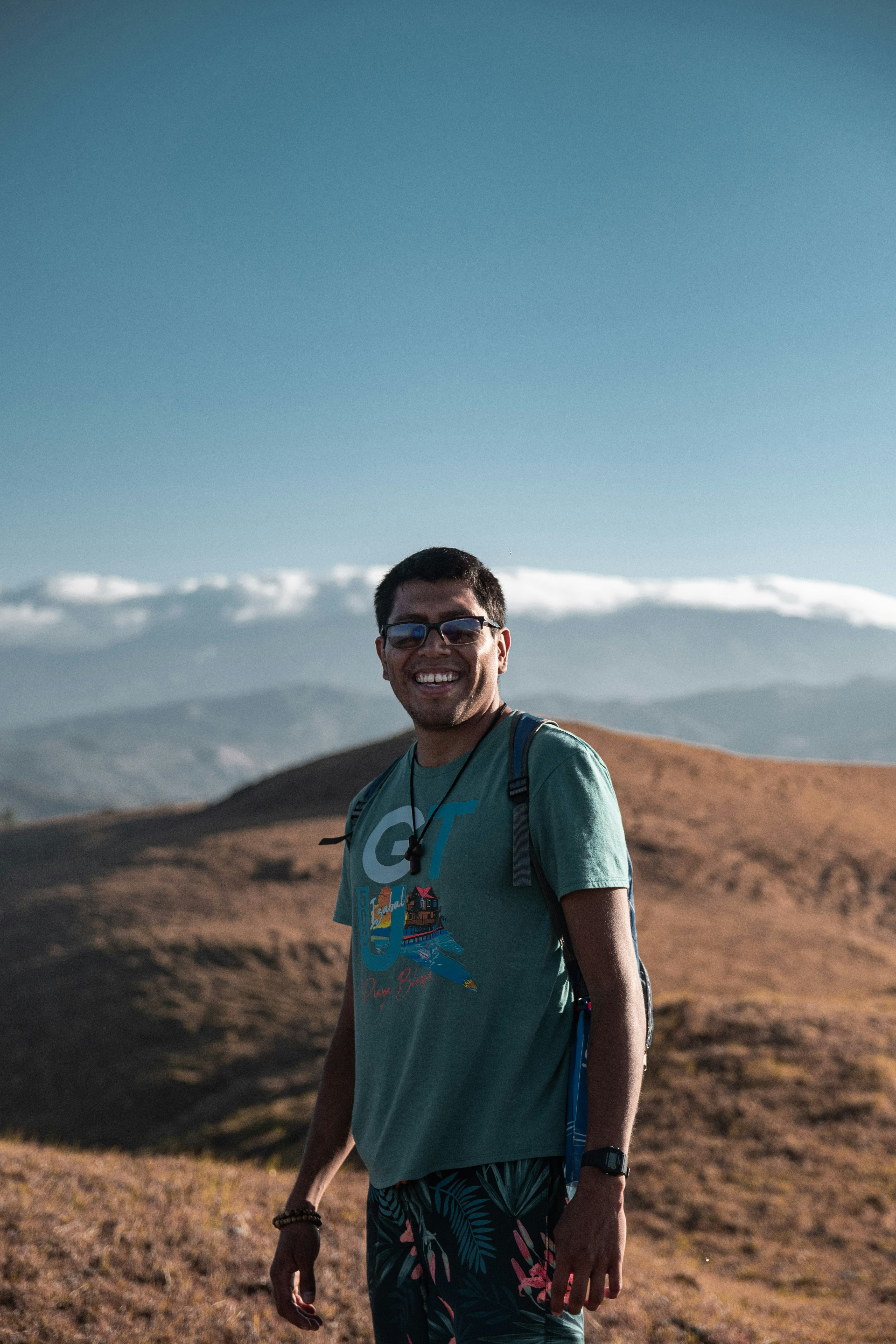 Julio Anibal Car fue mi compañero jesuita desde el noviciado. Salió de la Compañía de Jesús, pero siempre recuerdo con cuánto cariño rebalsa su corazón y sonrisa cuando subíamos cordilleras, cerros y montañas. Su profundidad en afectos permite que guste internamente la vida. ¡Que siempre sea todo para Mayor Gloria de Dios! | Man smiling on a grassy hilltop with mountains behind