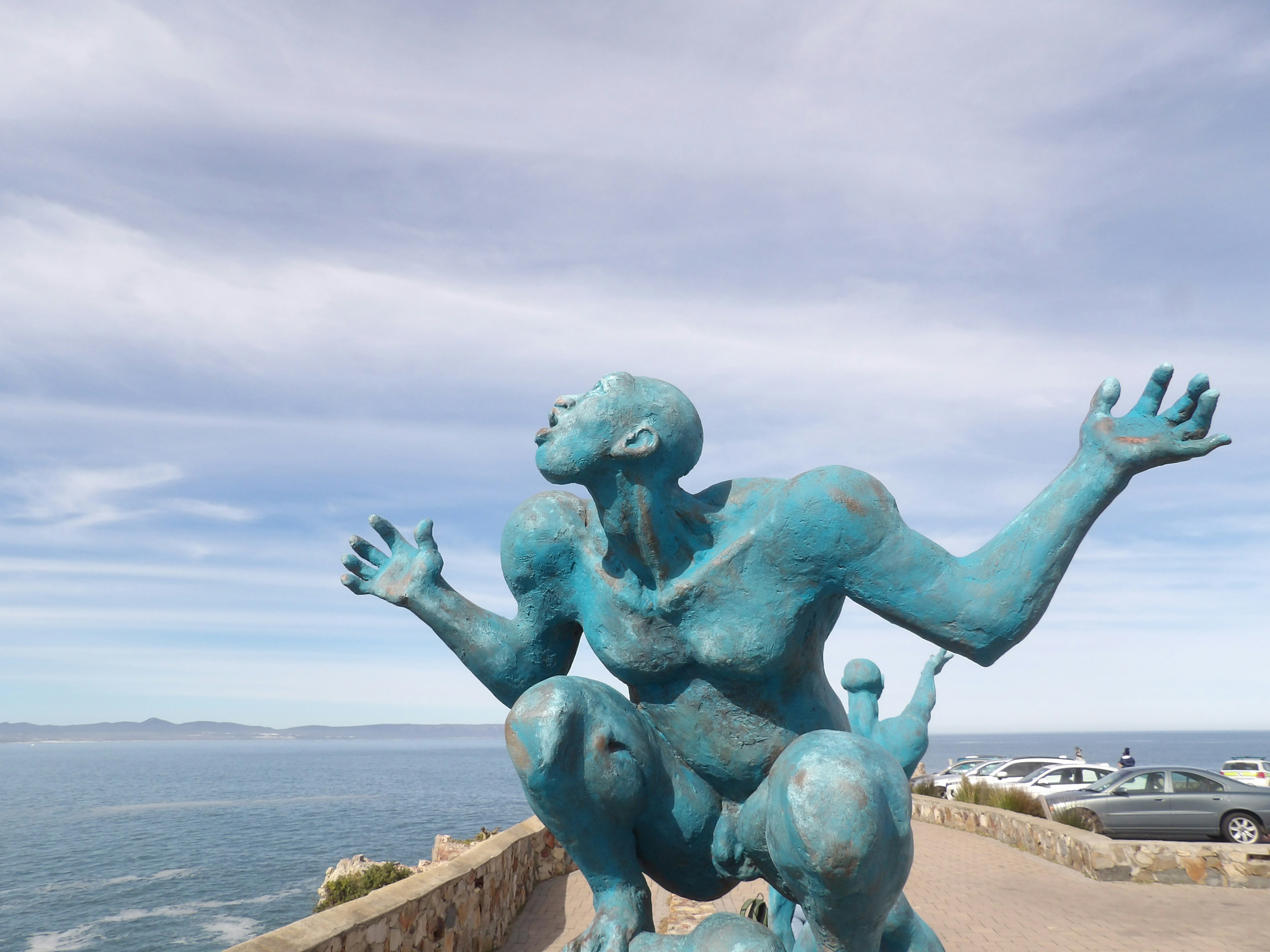 Bronze sculpture of a human figure in a dynamic pose, set against a coastal backdrop. The artwork embodies themes of liberation and emotion.