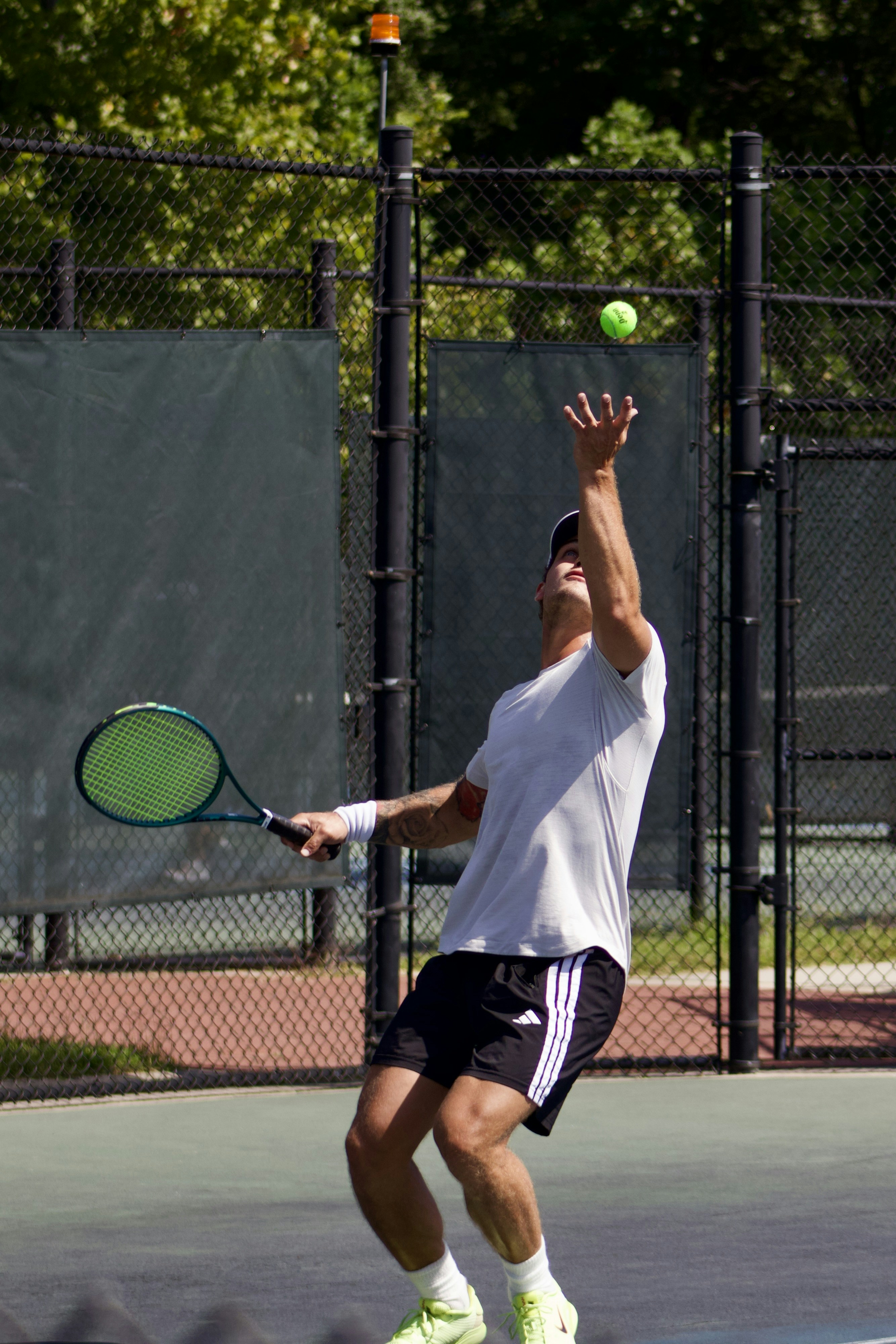 Athlete preparing to serve a tennis ball, showcasing focus and athleticism on a court surrounded by fencing.