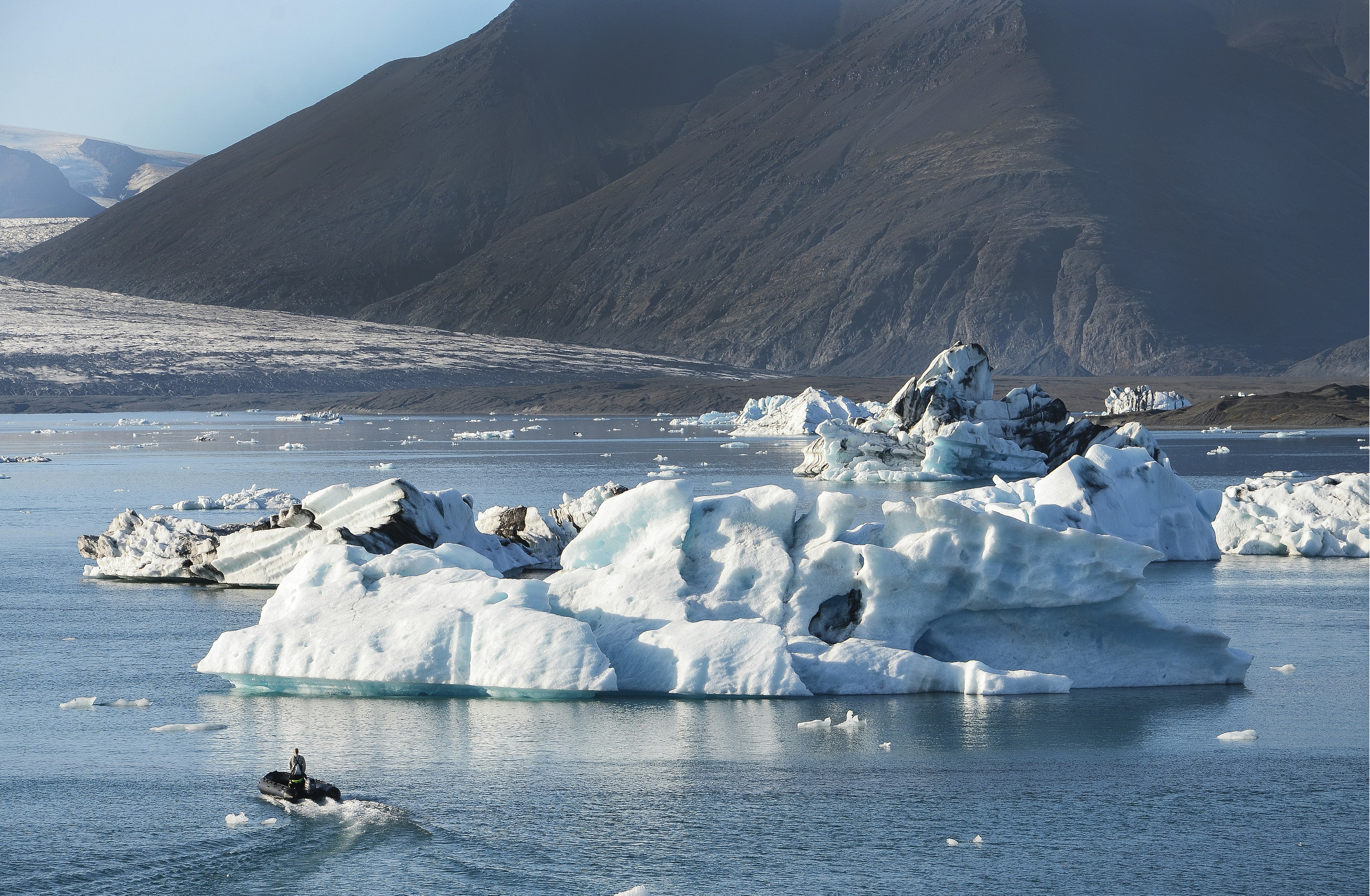 Glacial Lullaby: A lone boat threads a sculpted iceberg beneath shadowed cliffs
