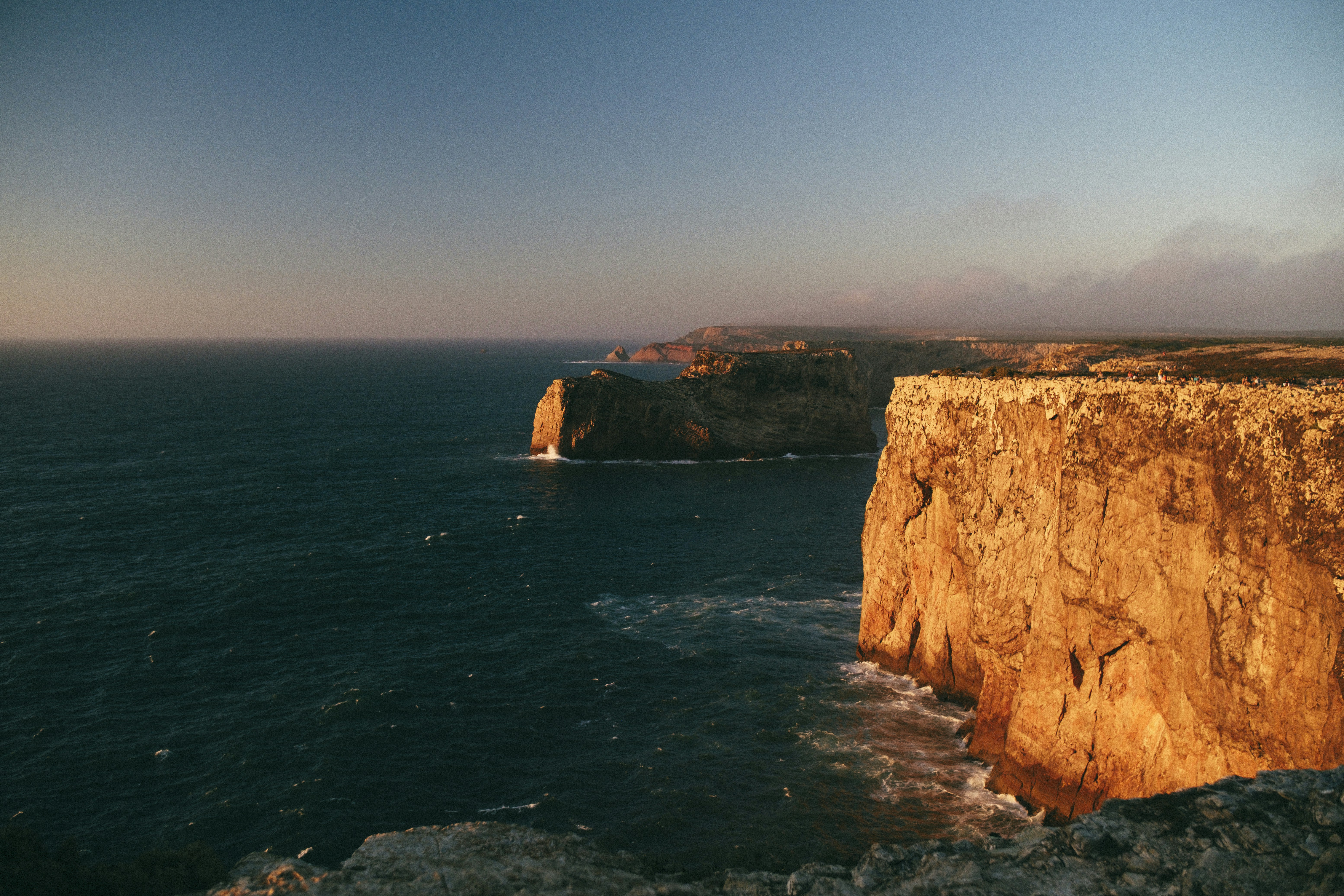 Golden cliffs overlooking a vast blue ocean at sunset.