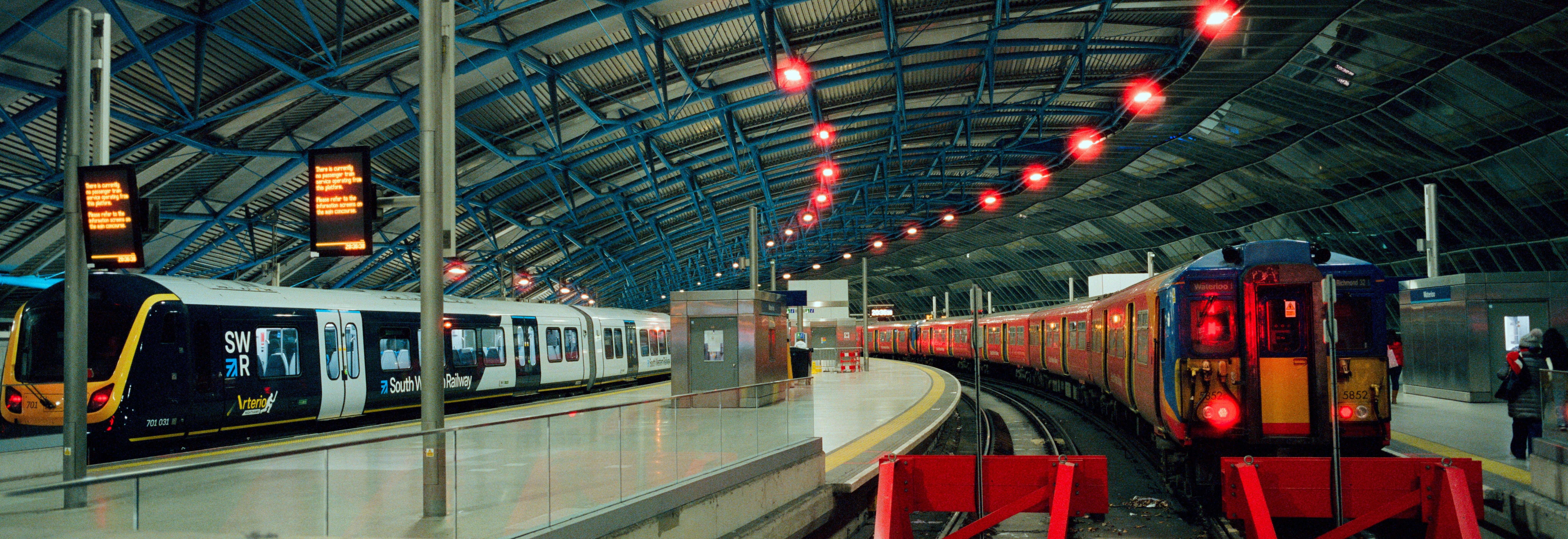 Panoramic view of a modern train station showcasing two trains on the platform beneath a striking blue ceiling with red lights.